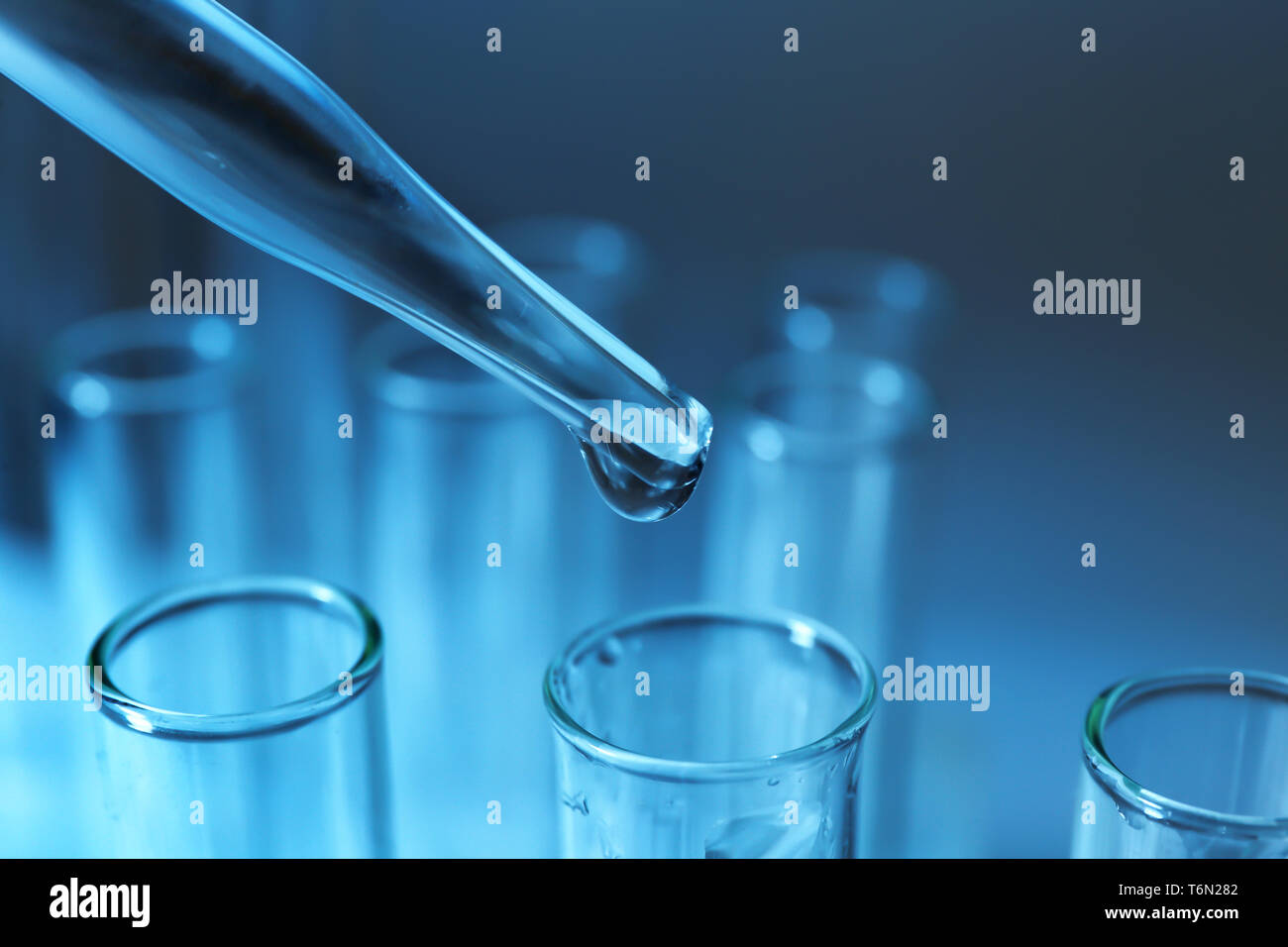 Pipette dripping sample into test tube on color background, closeup ...