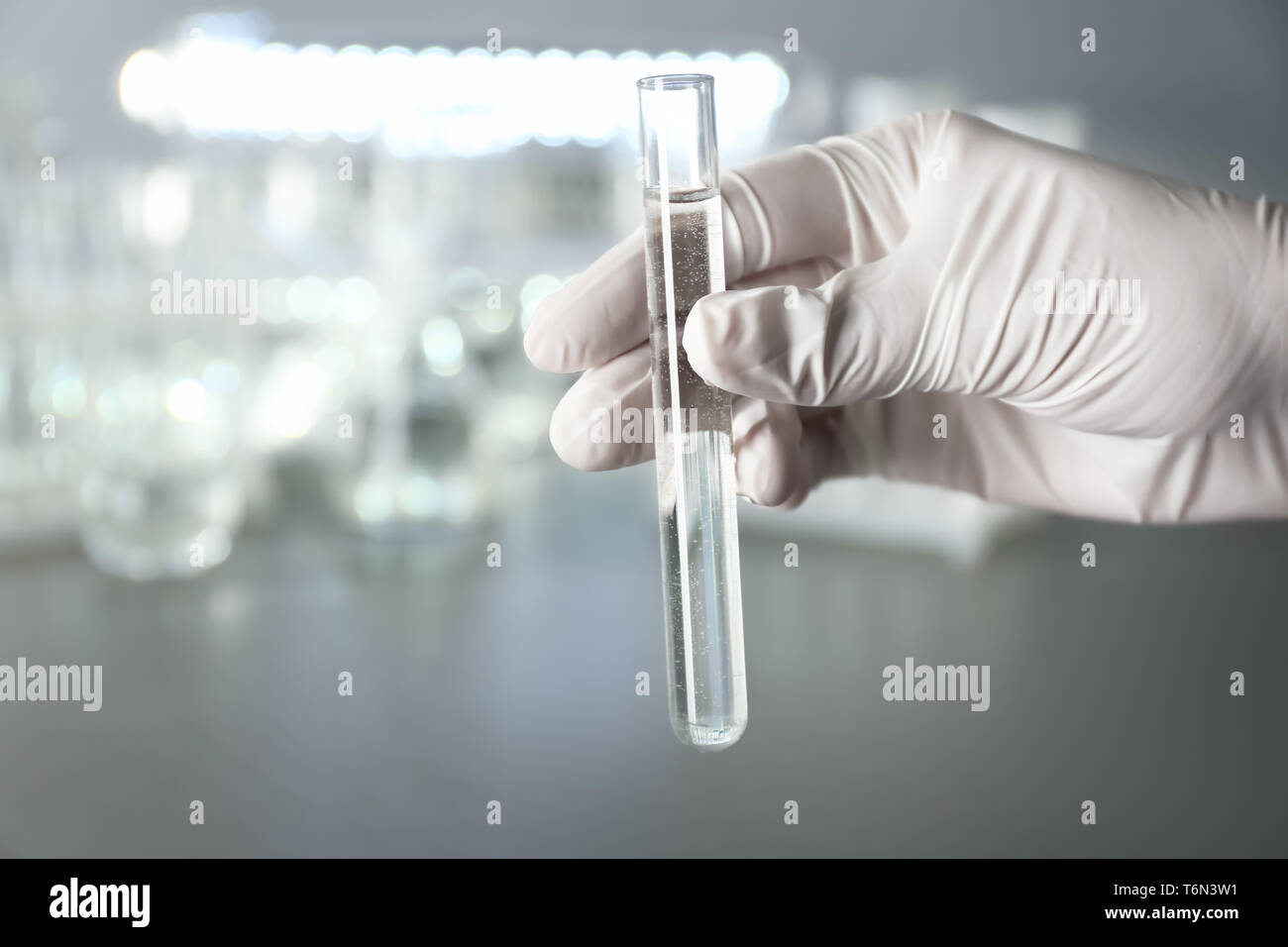 Laboratory worker holding test tube with water on blurred background ...
