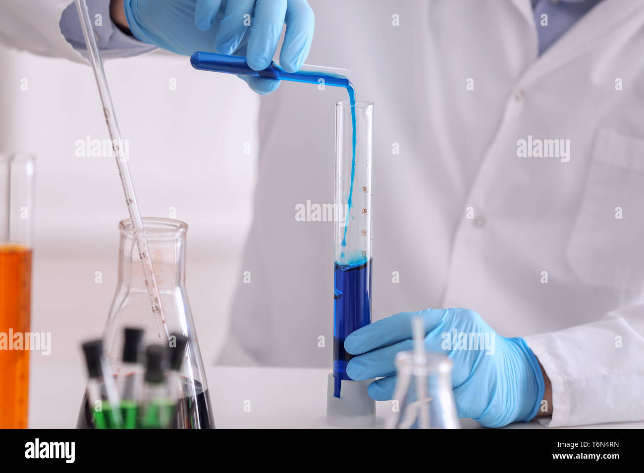 Scientist pouring color sample into graduated cylinder in laboratory ...