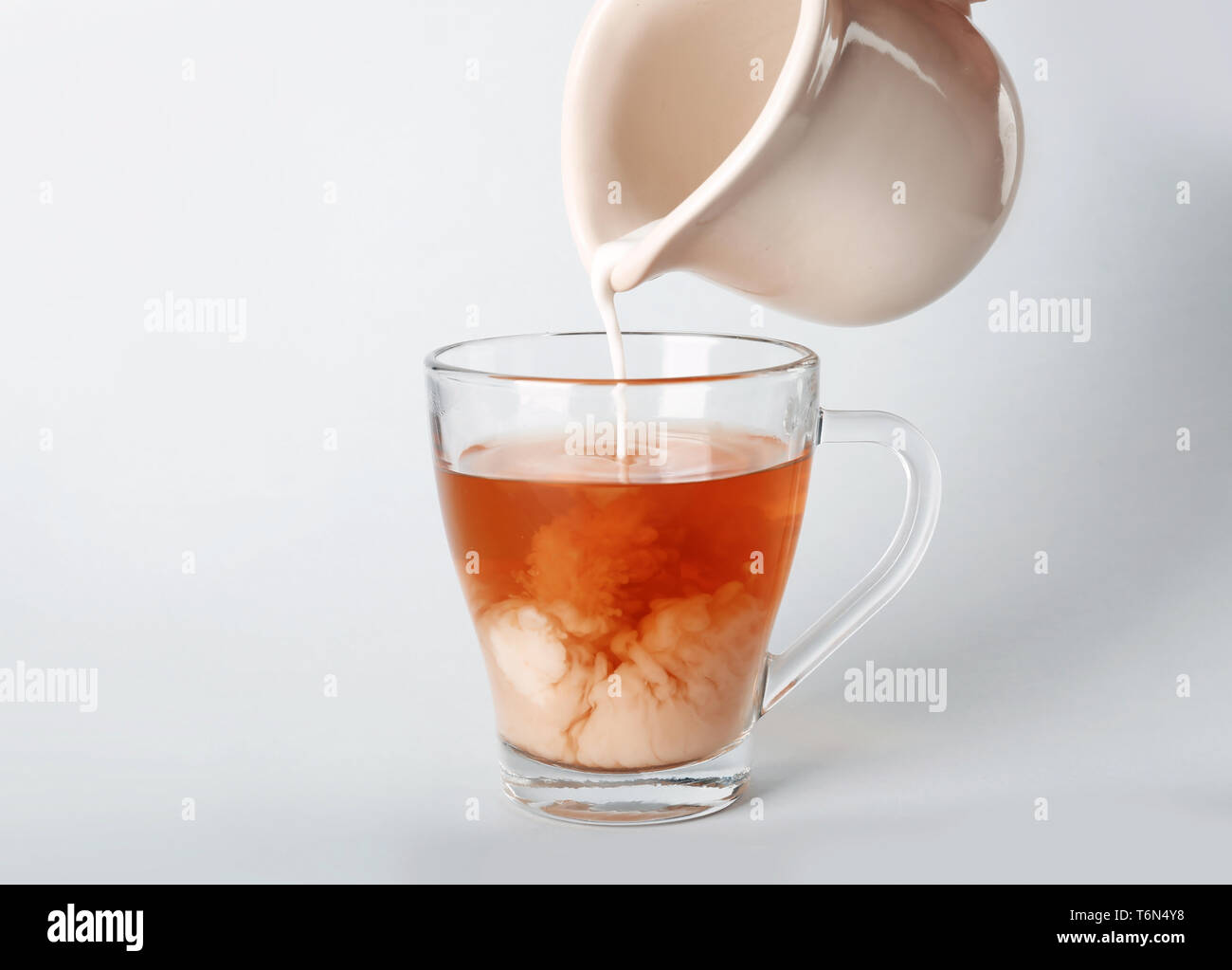 Pouring of milk into glass cup with tea on light background Stock Photo ...