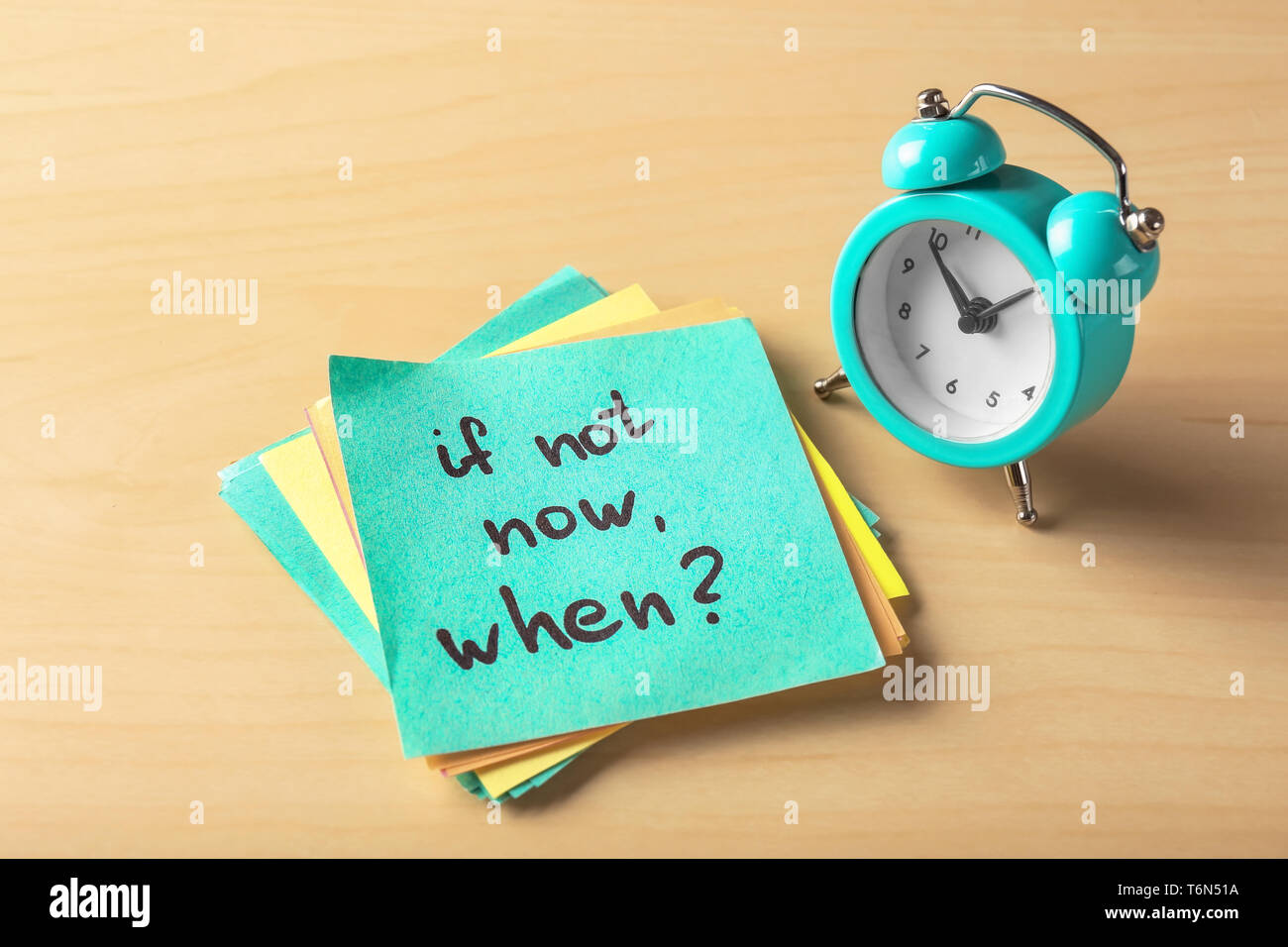 Sticker with phrase "If not now, when?" and alarm clock on table. Time ...