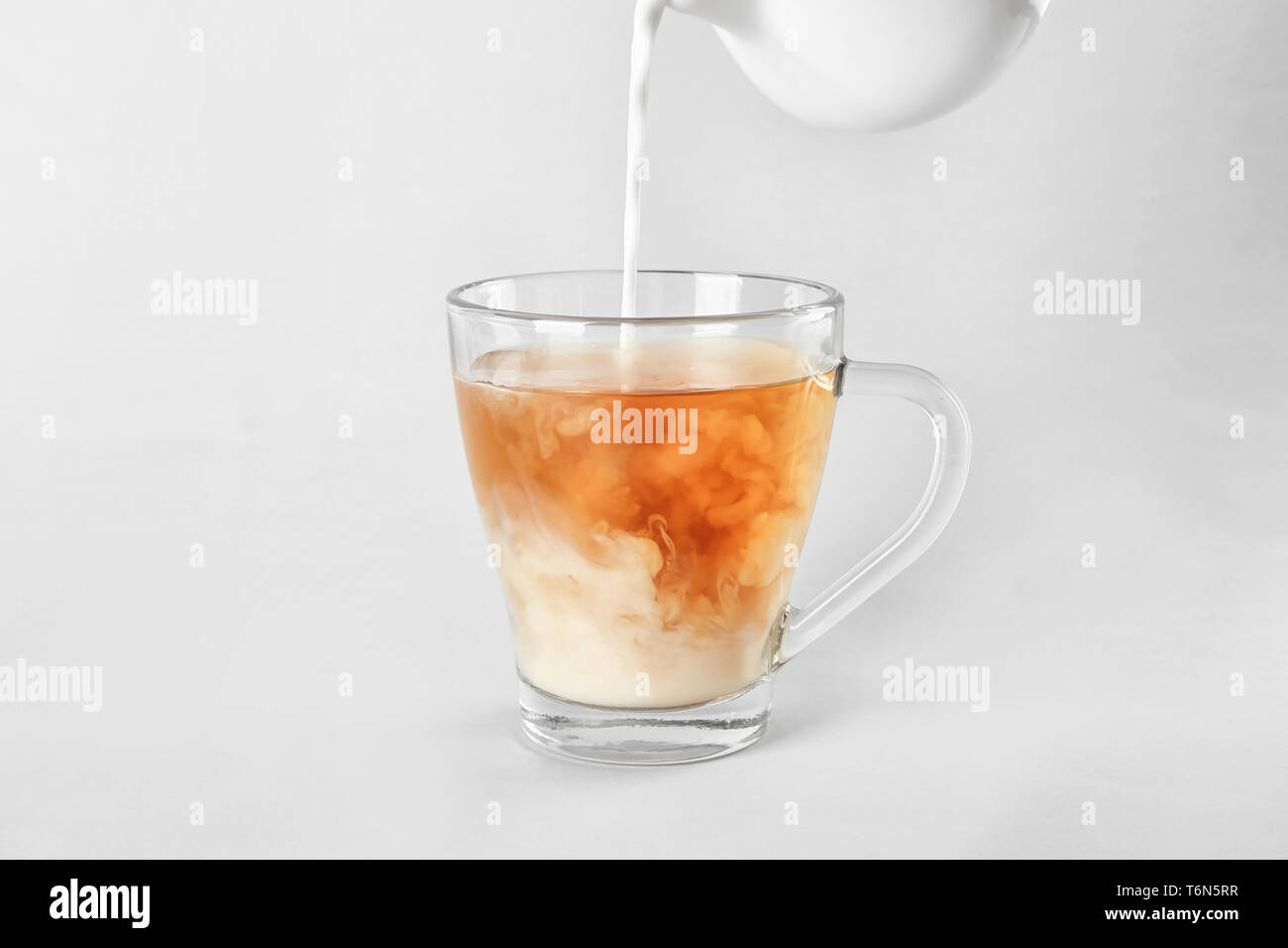 Adding milk to delicious tea on light background Stock Photo - Alamy