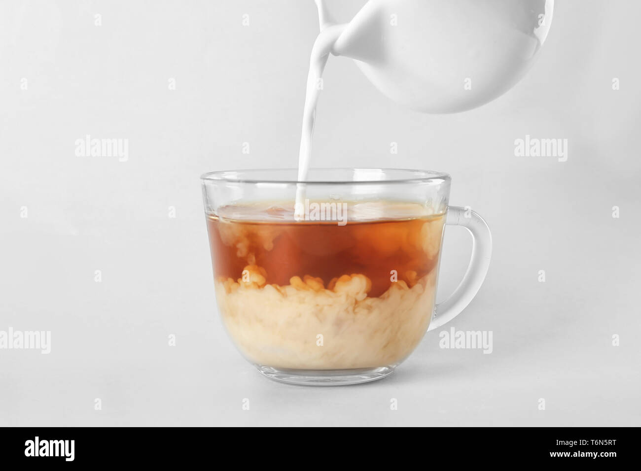 Adding milk to delicious tea on light background Stock Photo - Alamy