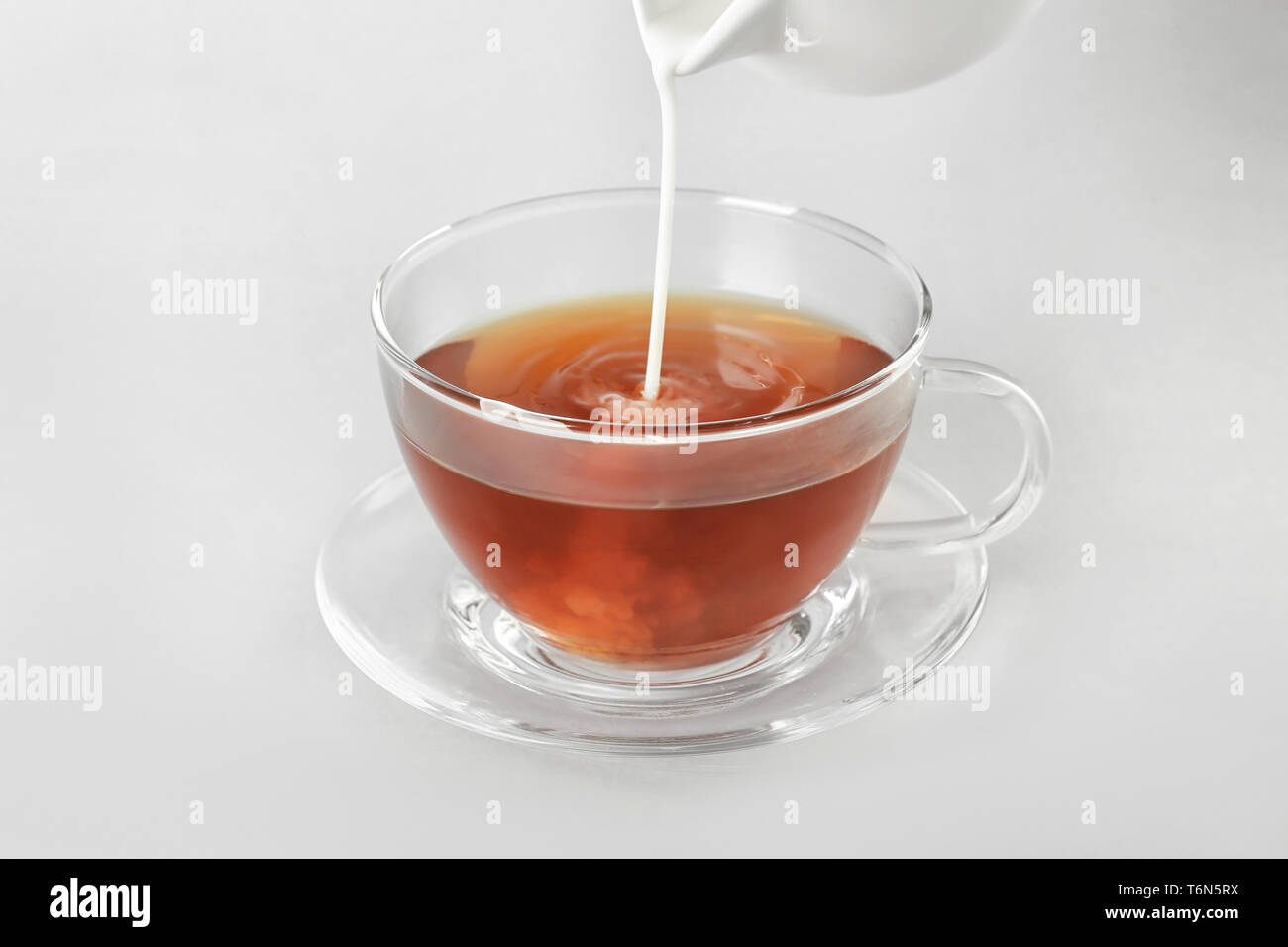 Adding milk to delicious tea on light background Stock Photo - Alamy