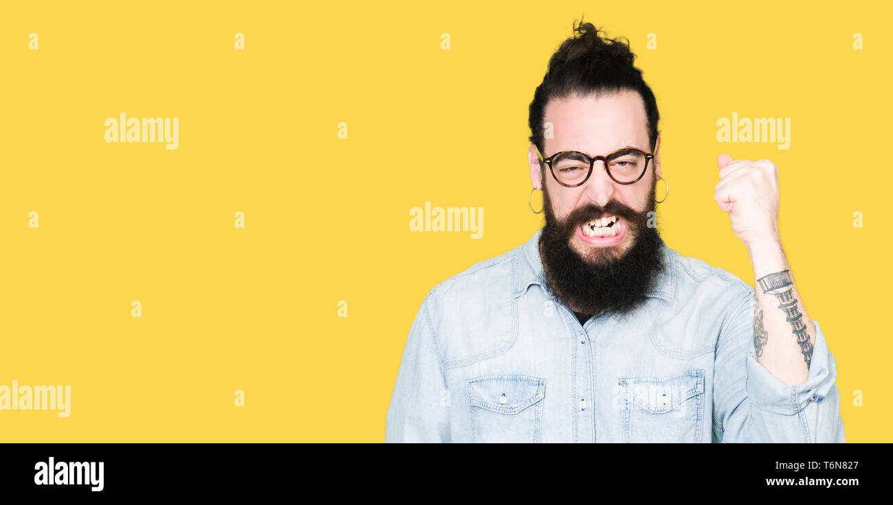 Young hipster man with long hair and beard wearing glasses angry and ...
