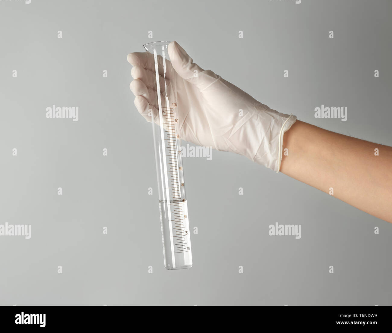 Laboratory worker holding graduated cylinder with water on grey ...