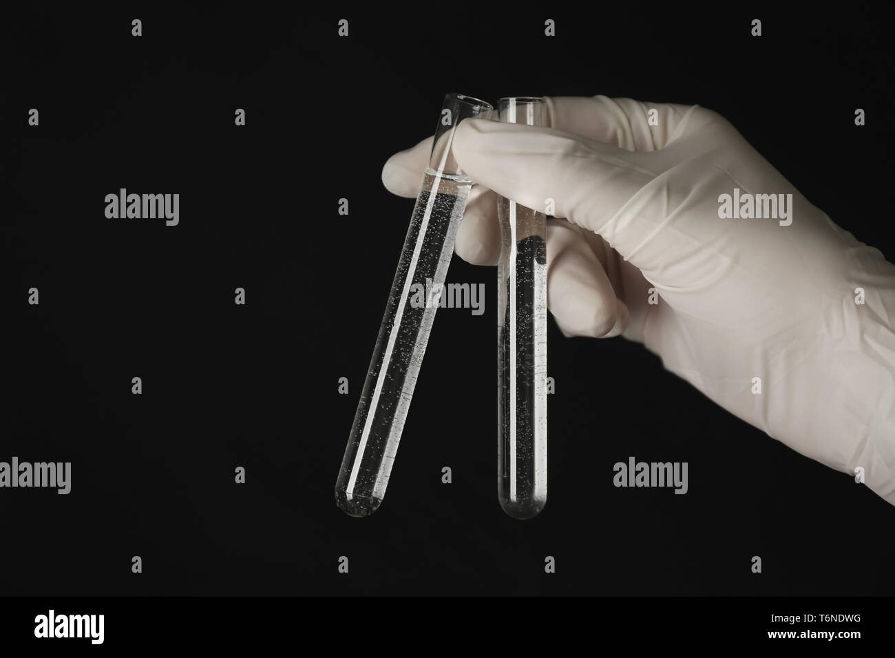 Laboratory worker holding test tubes with water on black background ...