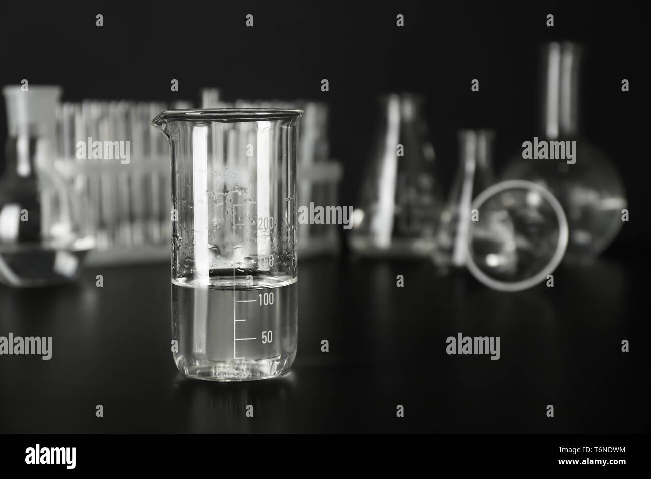 Beaker and test tubes with water on table against black background ...