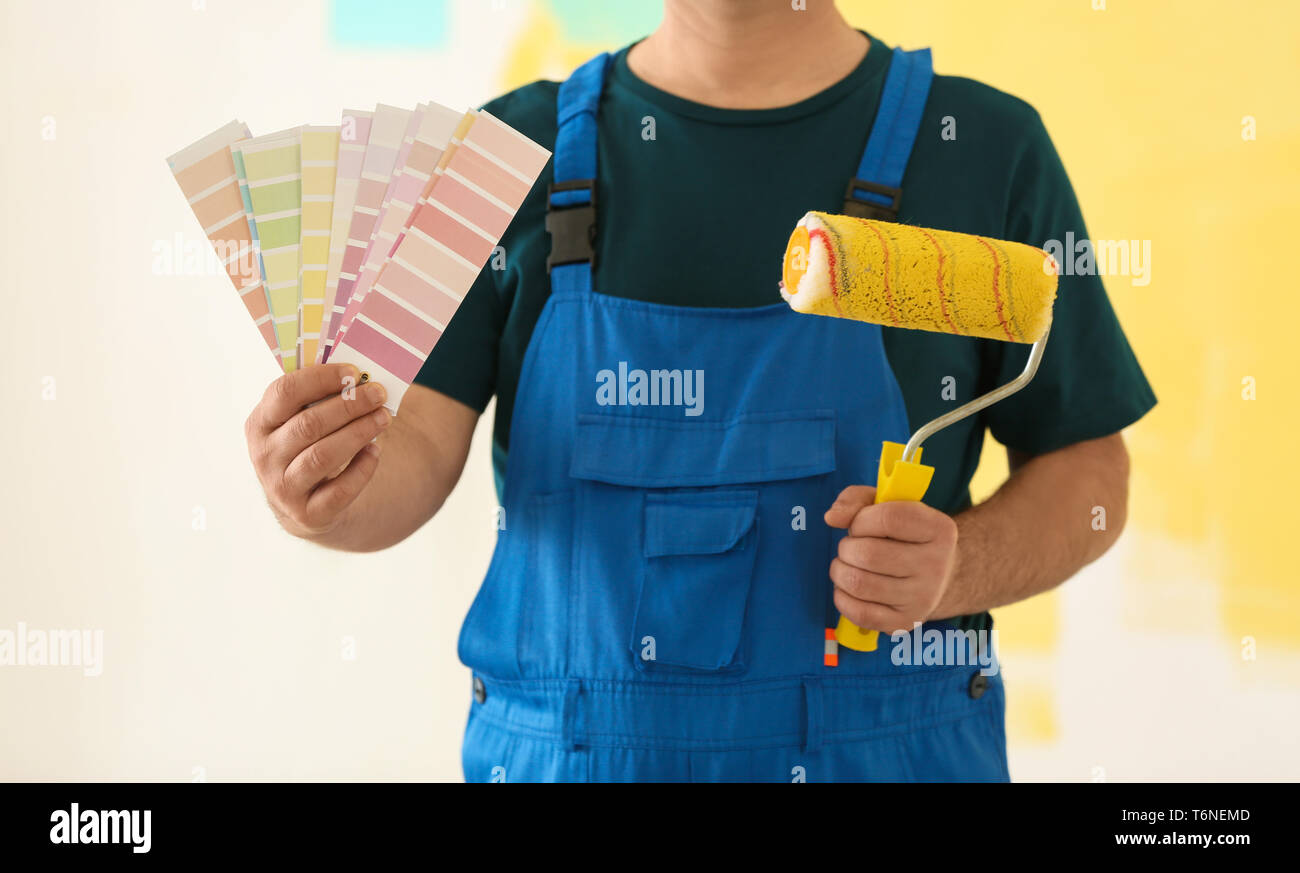 Male painter in uniform with color palette samples and roller brush on ...