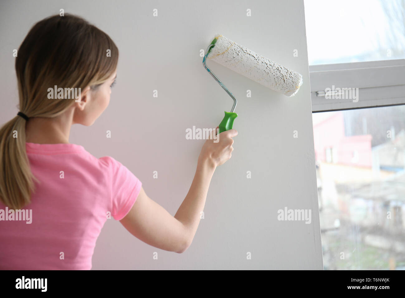 Female painter using roller for refurbishing color of wall indoors ...