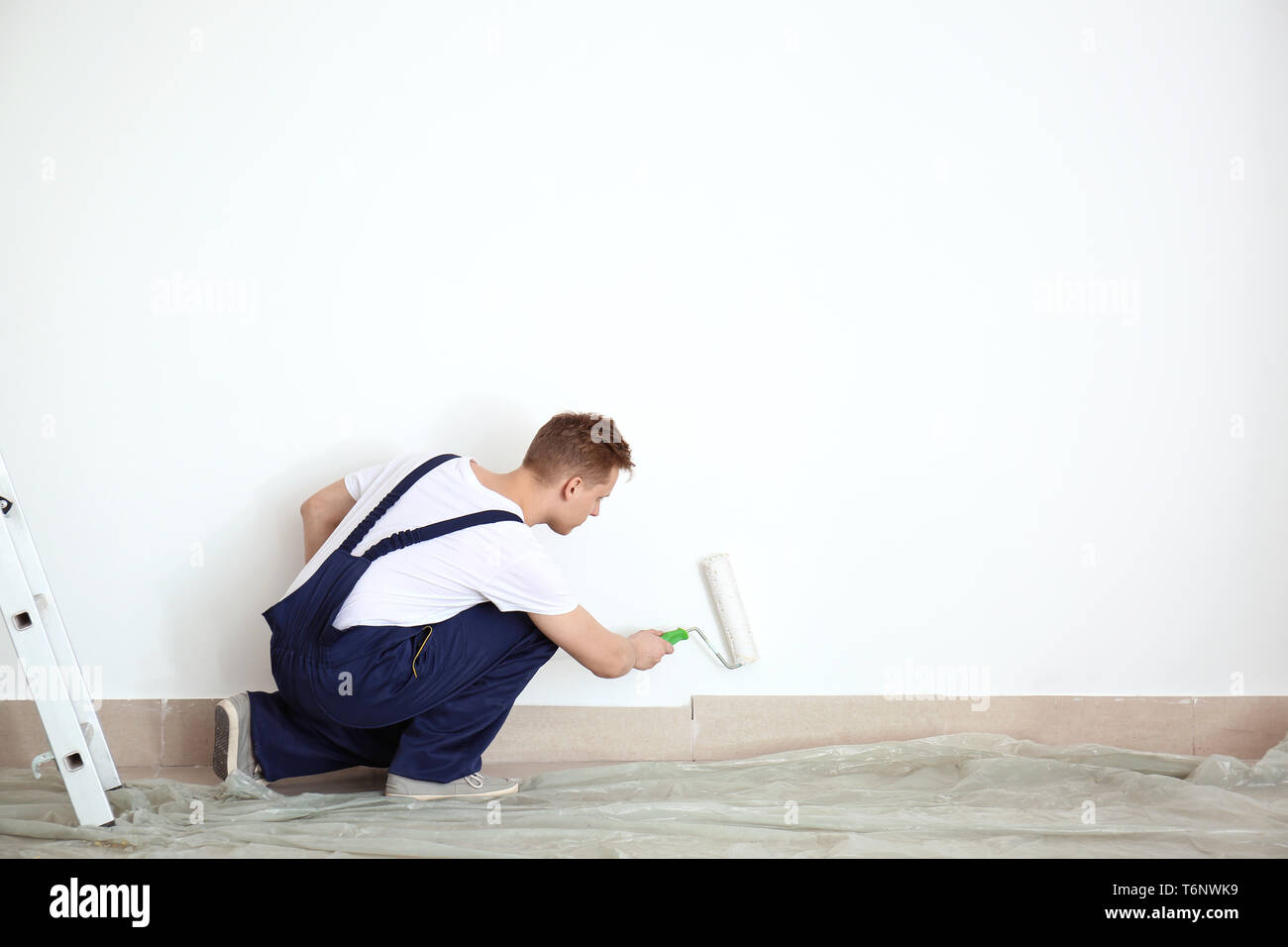 Male painter using roller for refurbishing color of wall indoors Stock ...