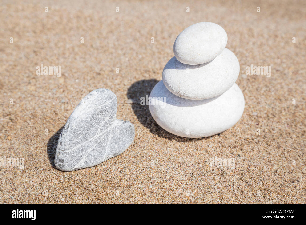 heart shaped stone and stack of pebbles on balance on a sandy beach ...