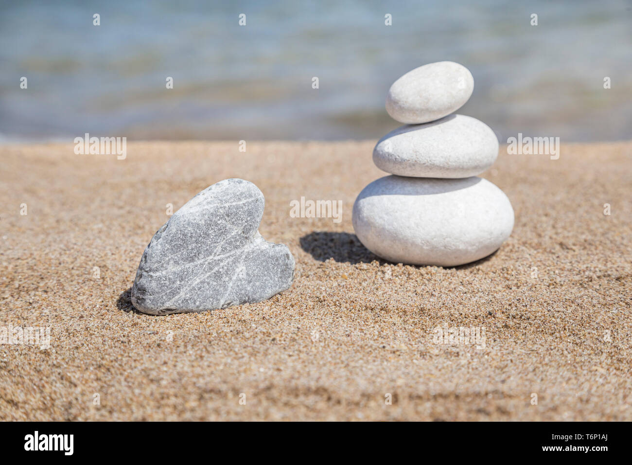 heart shaped stone and stack of pebbles on balance on a sandy beach ...
