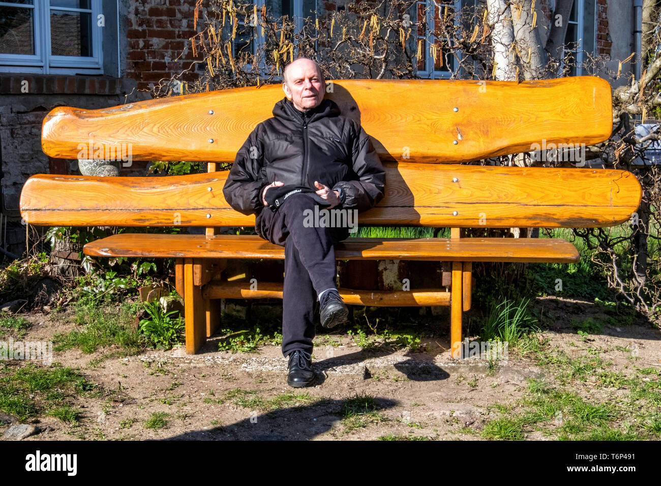 Senior elderly man sitting on wood bench at Gutshaus Manor House estate ...