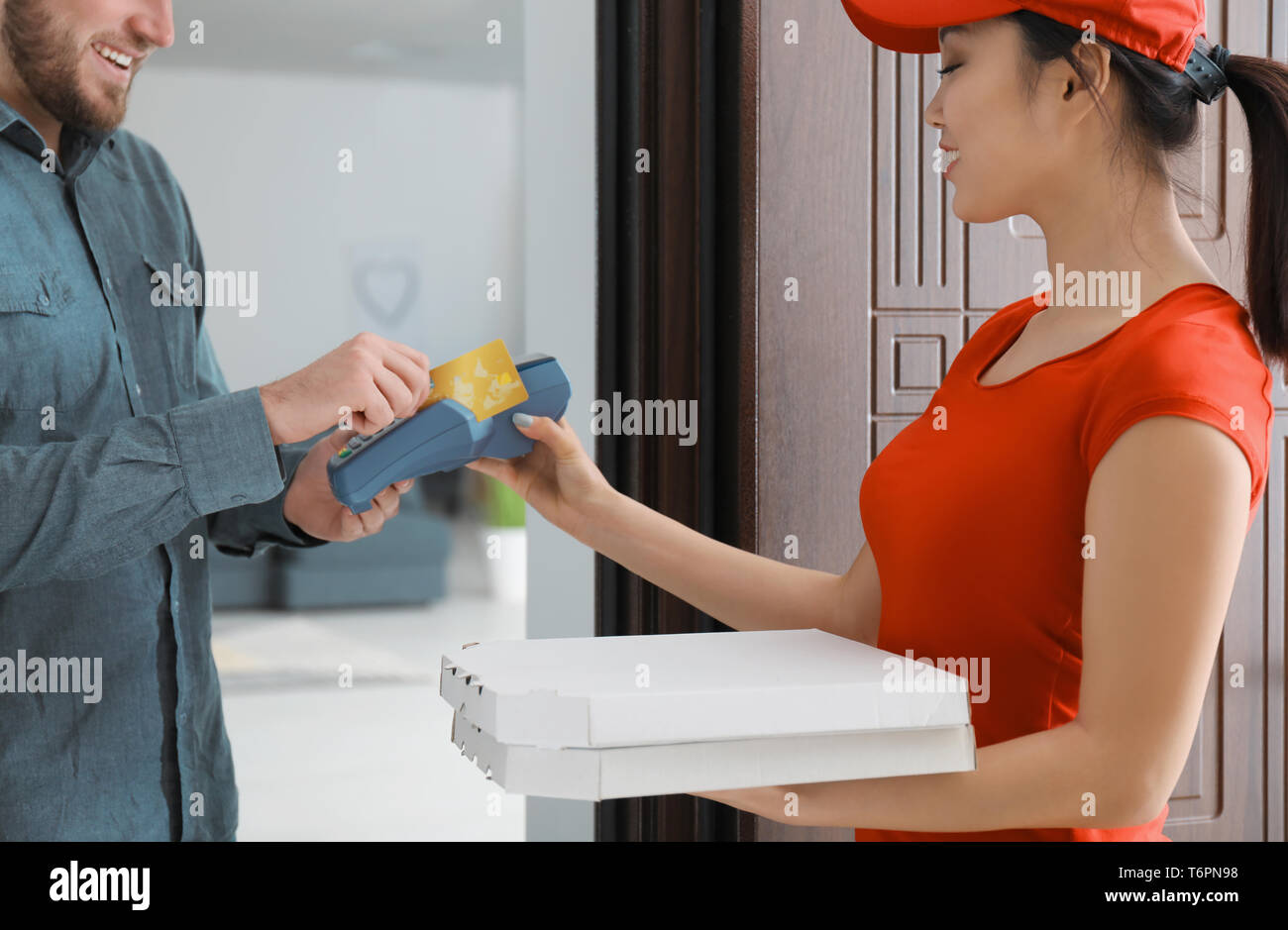 Young man using bank terminal for credit card payment at doorway. Food ...