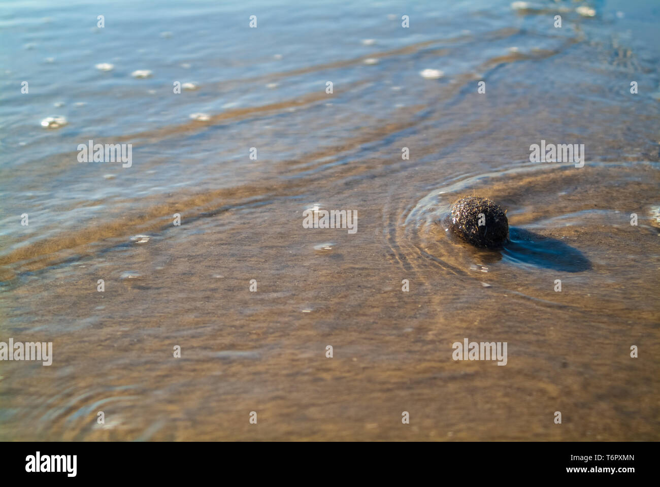 Geometric shape ball on the beach sand immerged in a crystal clear pure ...