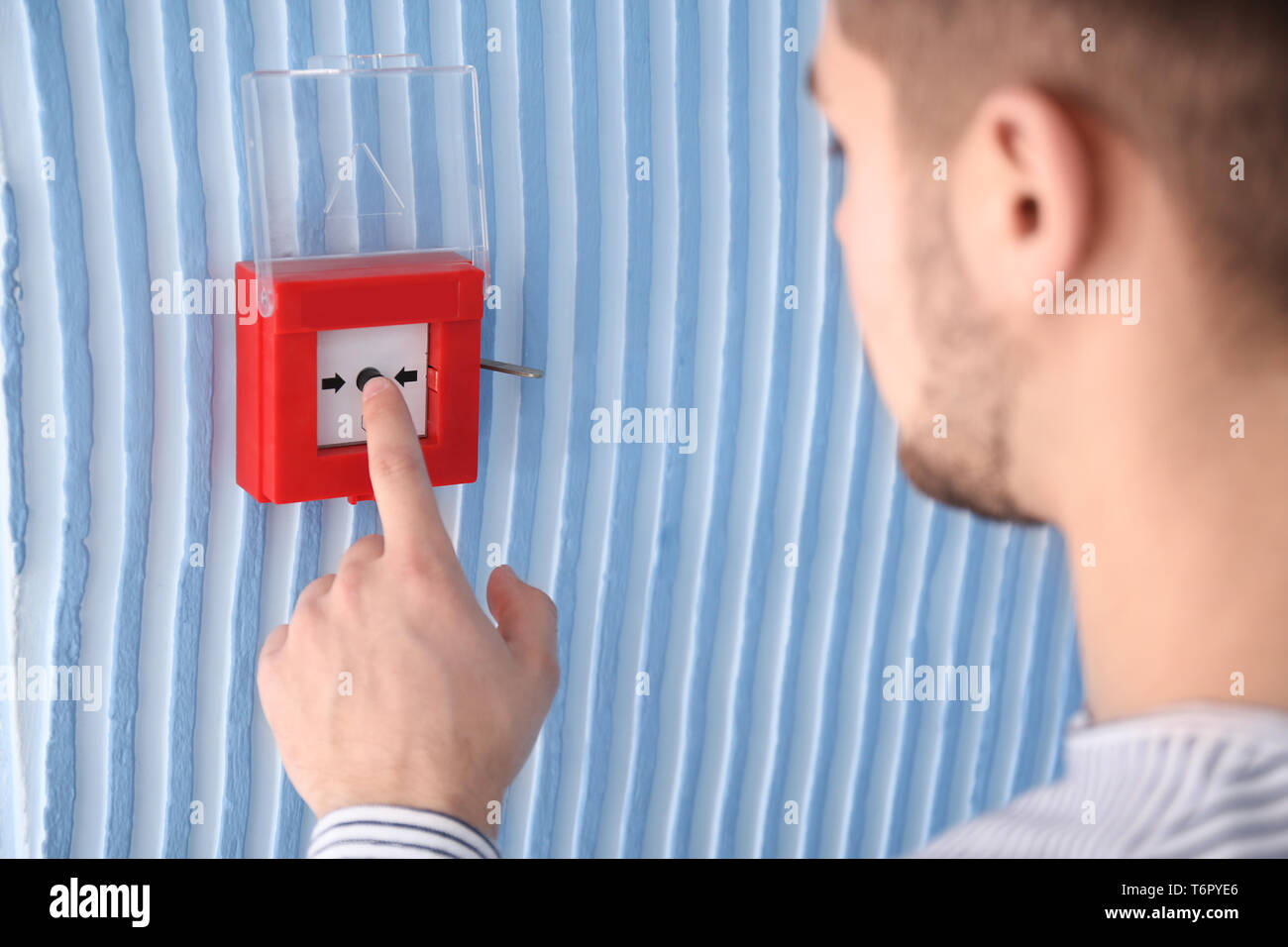 Young man pushing button of fire alarm system, indoors Stock Photo - Alamy