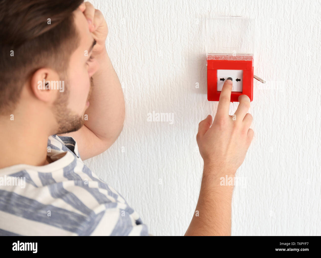 Young man pushing button of fire alarm system, indoors Stock Photo - Alamy