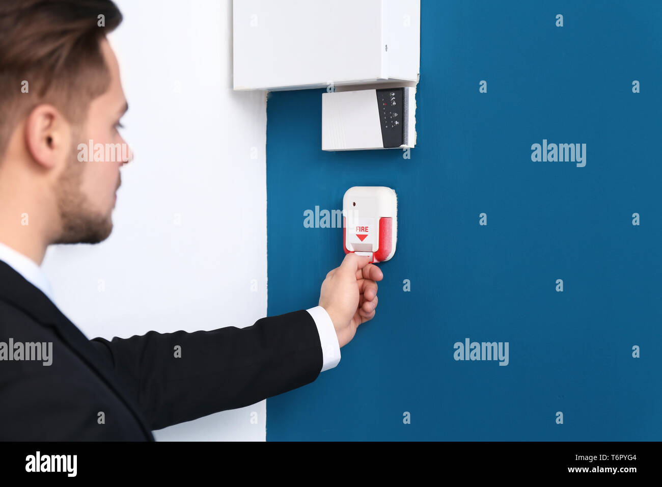 Young man pulling handle of fire alarm station, indoors Stock Photo - Alamy