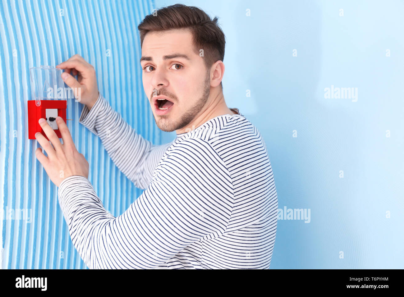 Young man pushing button of fire alarm system, indoors Stock Photo - Alamy