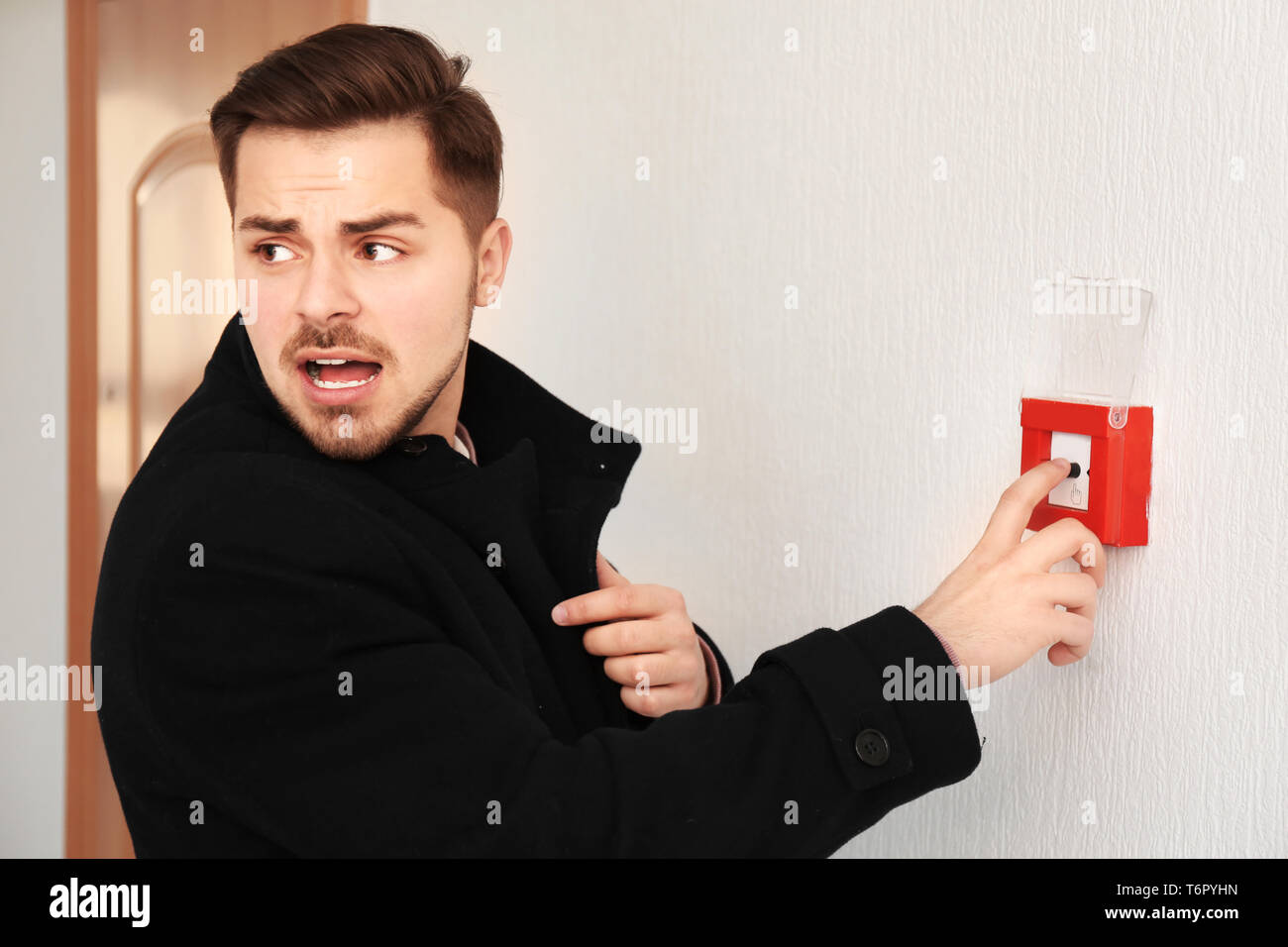 Young man pushing button of fire alarm system, indoors Stock Photo - Alamy