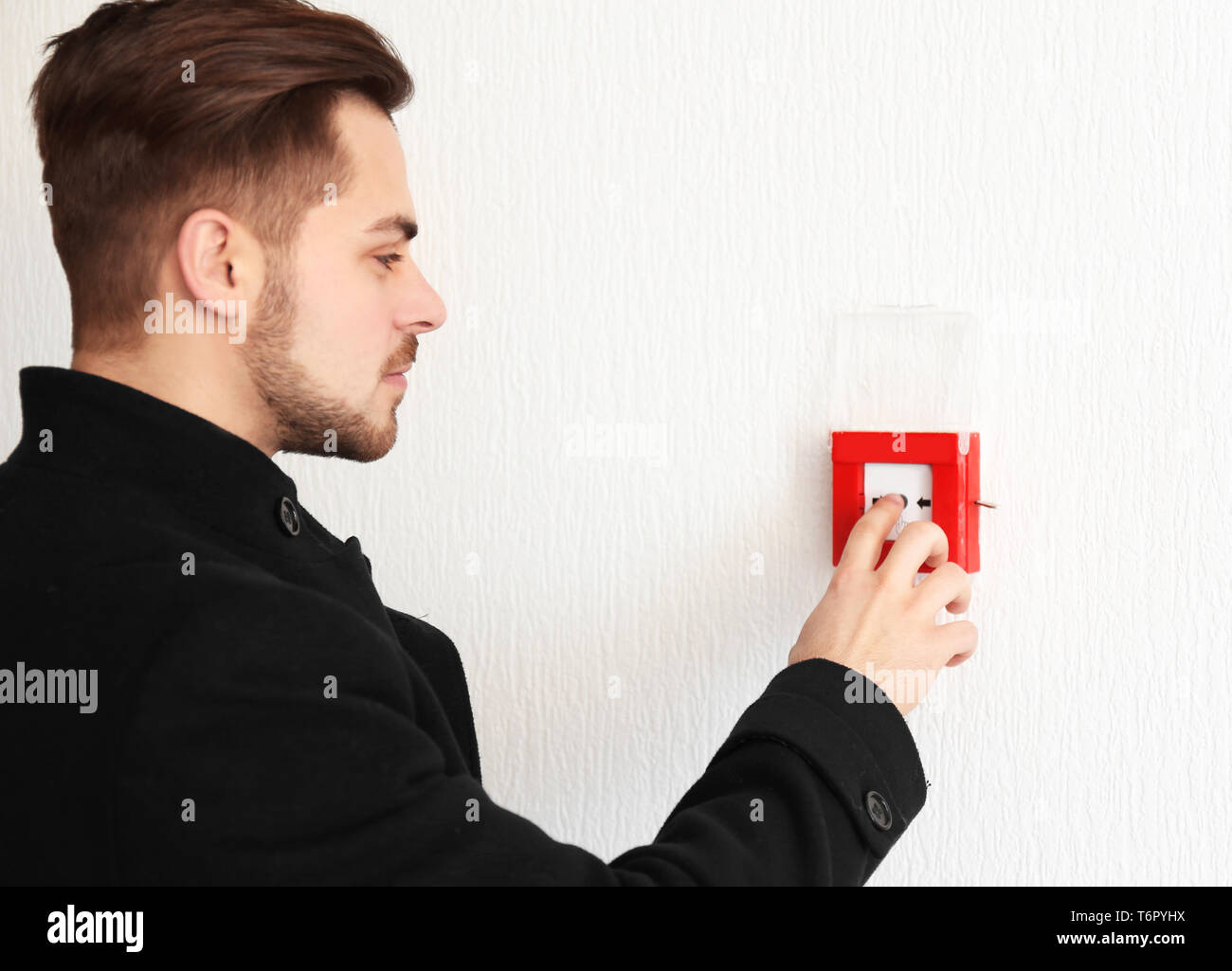 Young man pushing button of fire alarm system, indoors Stock Photo - Alamy