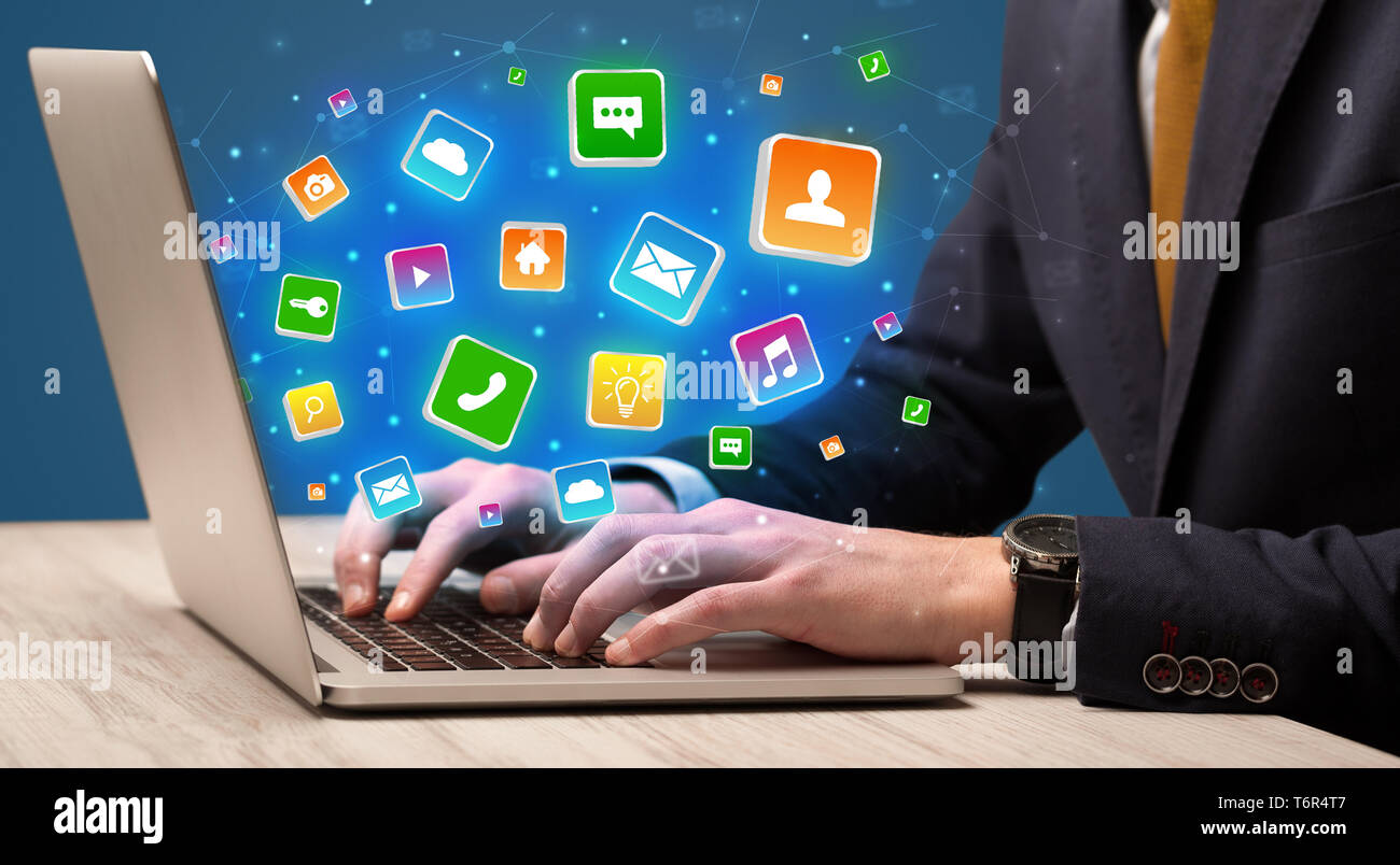 Businessman hand typing on laptop with flying application icons around ...