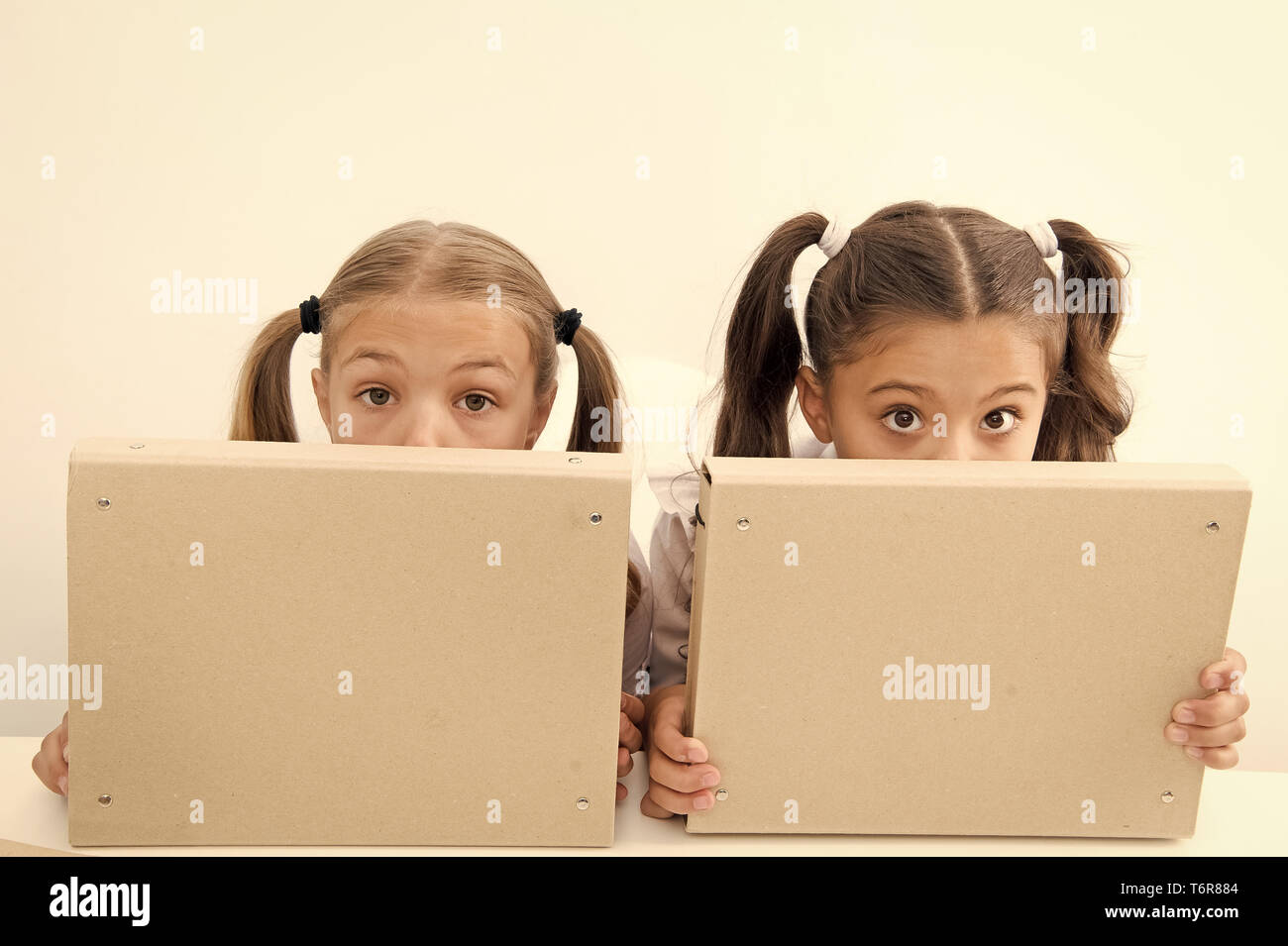 Little awkward girls hide faces behind file folders. Little awkward ...