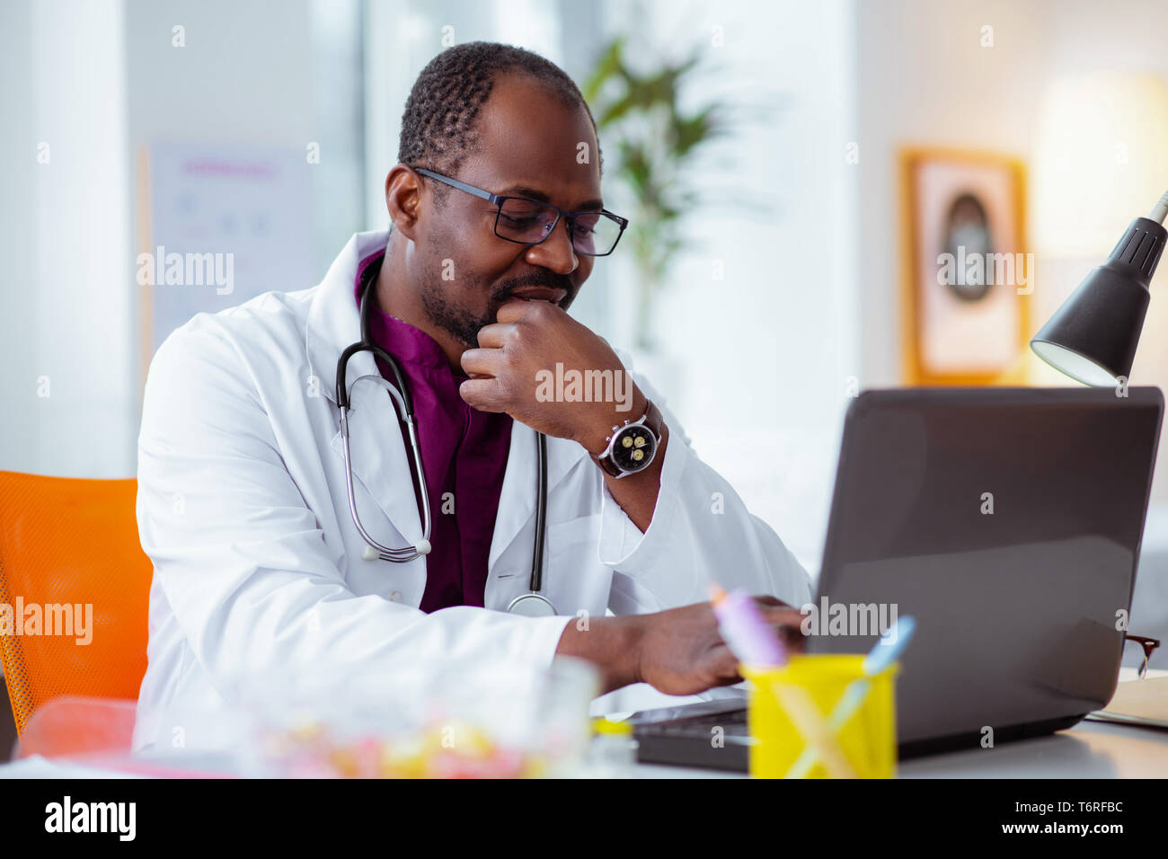 Dark-skinned doctor wearing glasses and watch feeling thoughtful Stock ...
