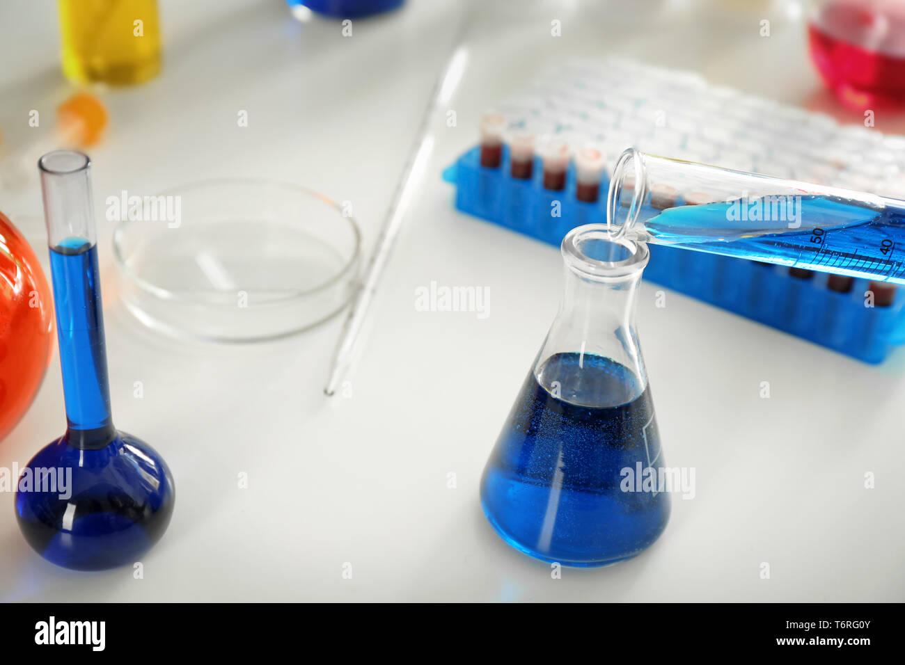 Pouring blue liquid from test tube into flask on table Stock Photo - Alamy