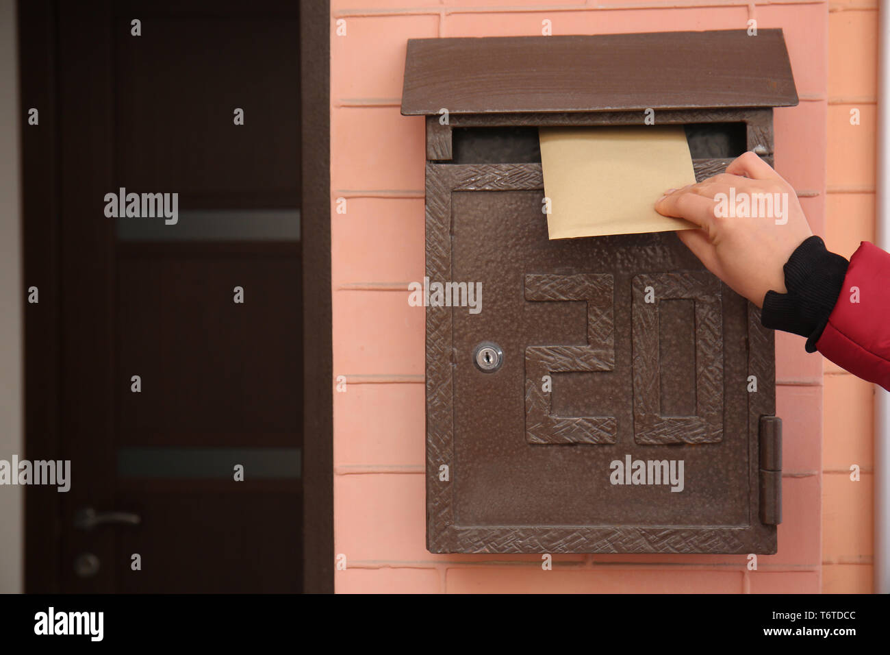 Woman putting envelope into mailbox on wall of building outdoors Stock ...
