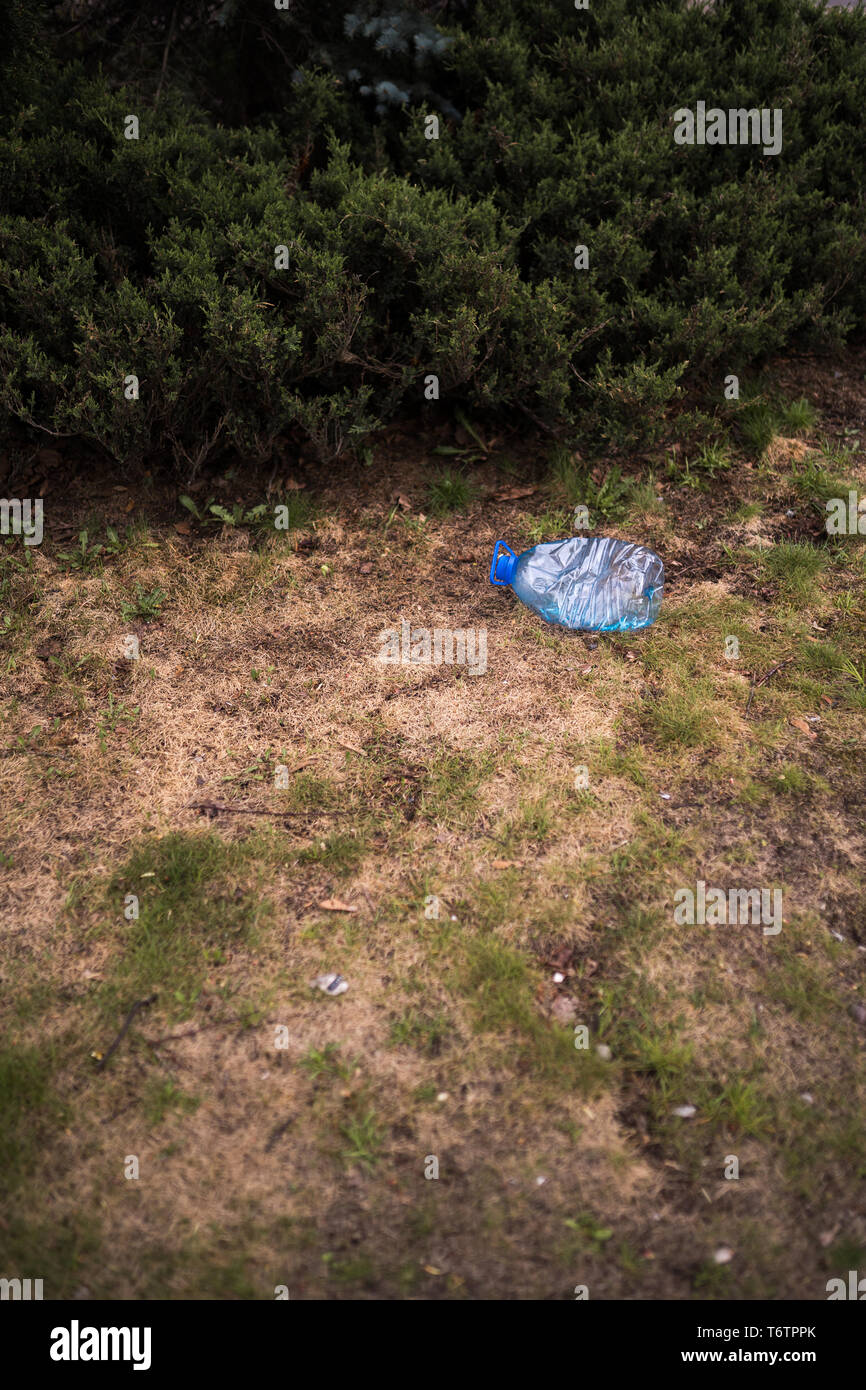 Blue big plastic bottle lying on the ground in tree in a park forest ...