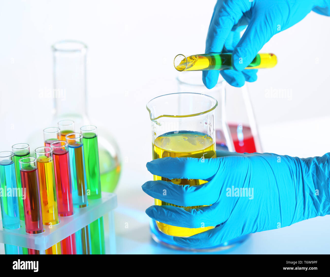 Laboratory worker pouring liquid from test tube into beaker on light ...