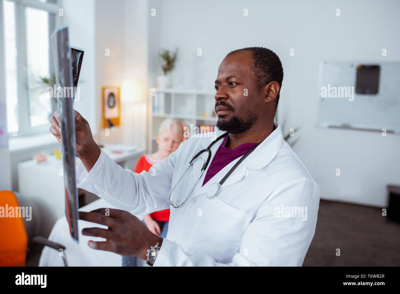 Dark-eyed doctor feeling concerned while checking x-ray of girl Stock ...