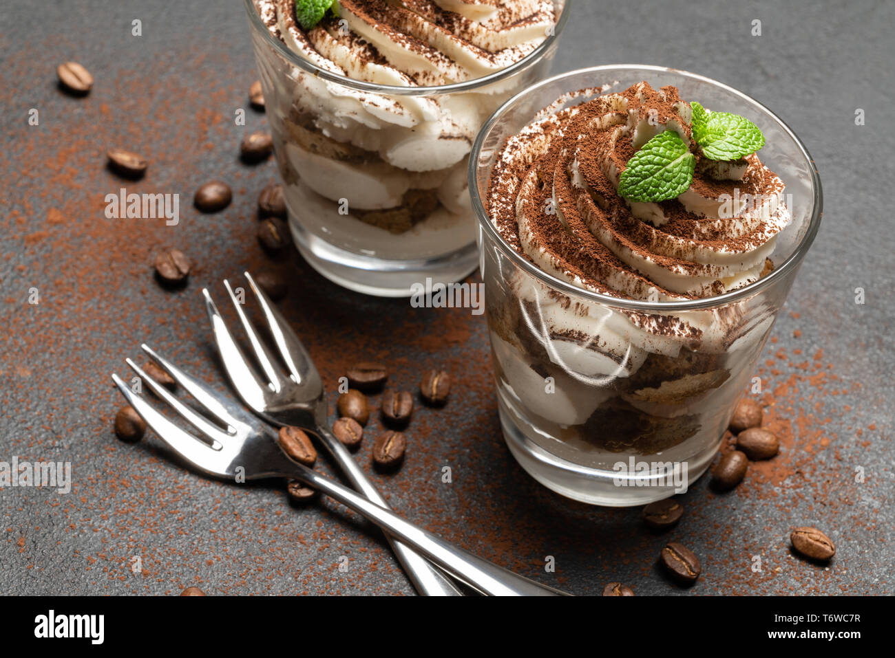 two portions Classic tiramisu dessert in a glass on dark concrete ...