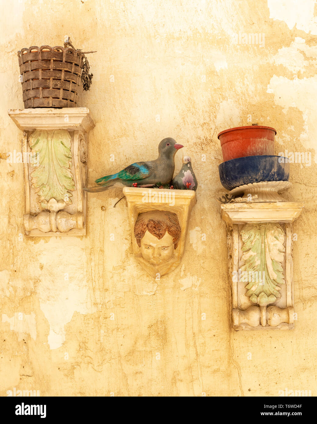 A pottery bird and plant pots sit on ornately carved corbels on a wall ...
