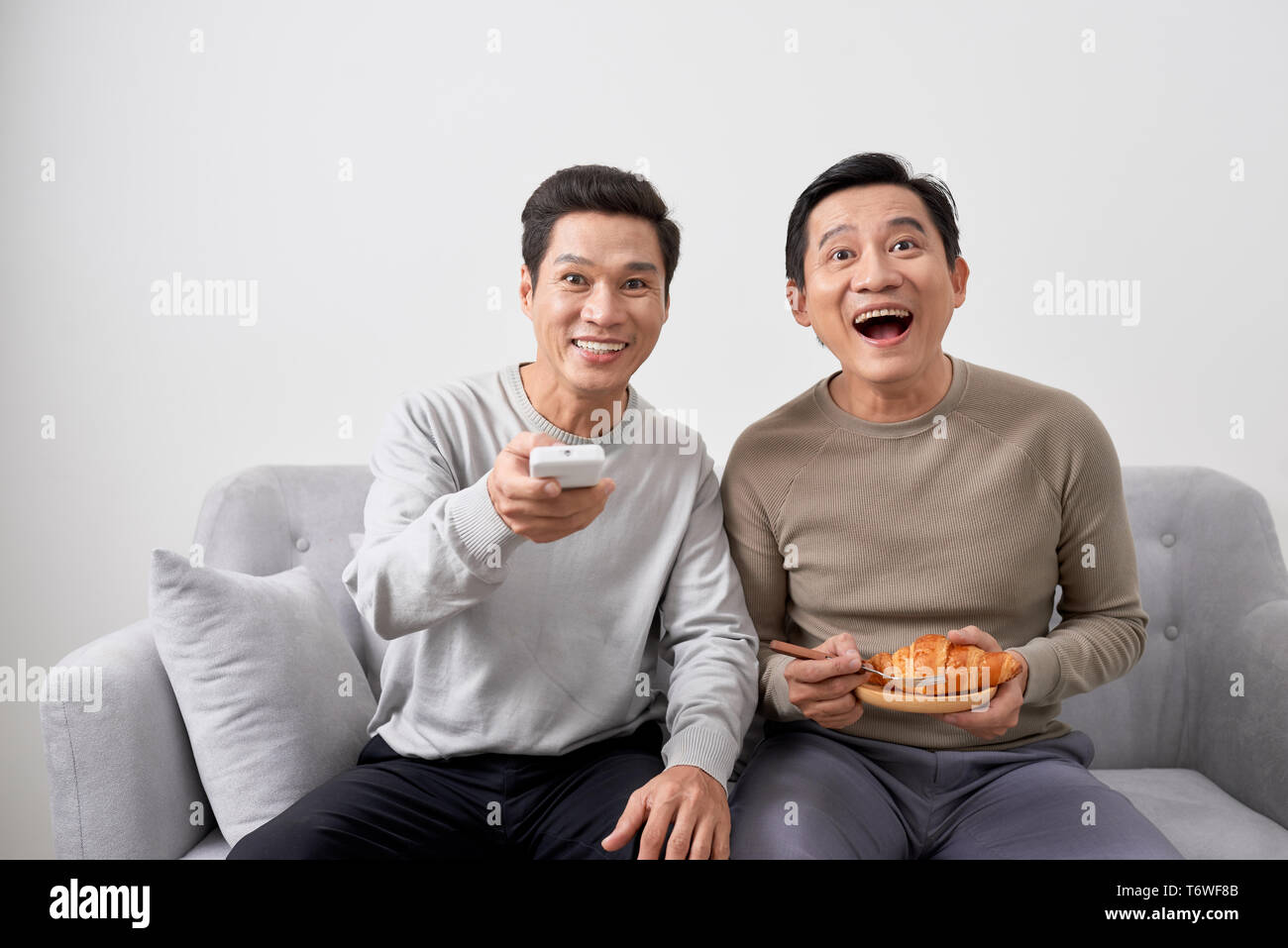 Men sitting on couch watching movie on television together at home ...