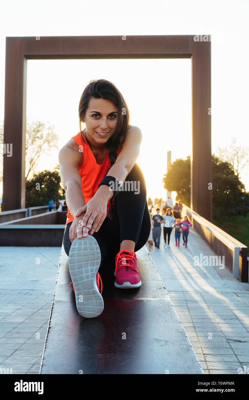 Young runner woman smiling stretching legs before run in a park. Close ...
