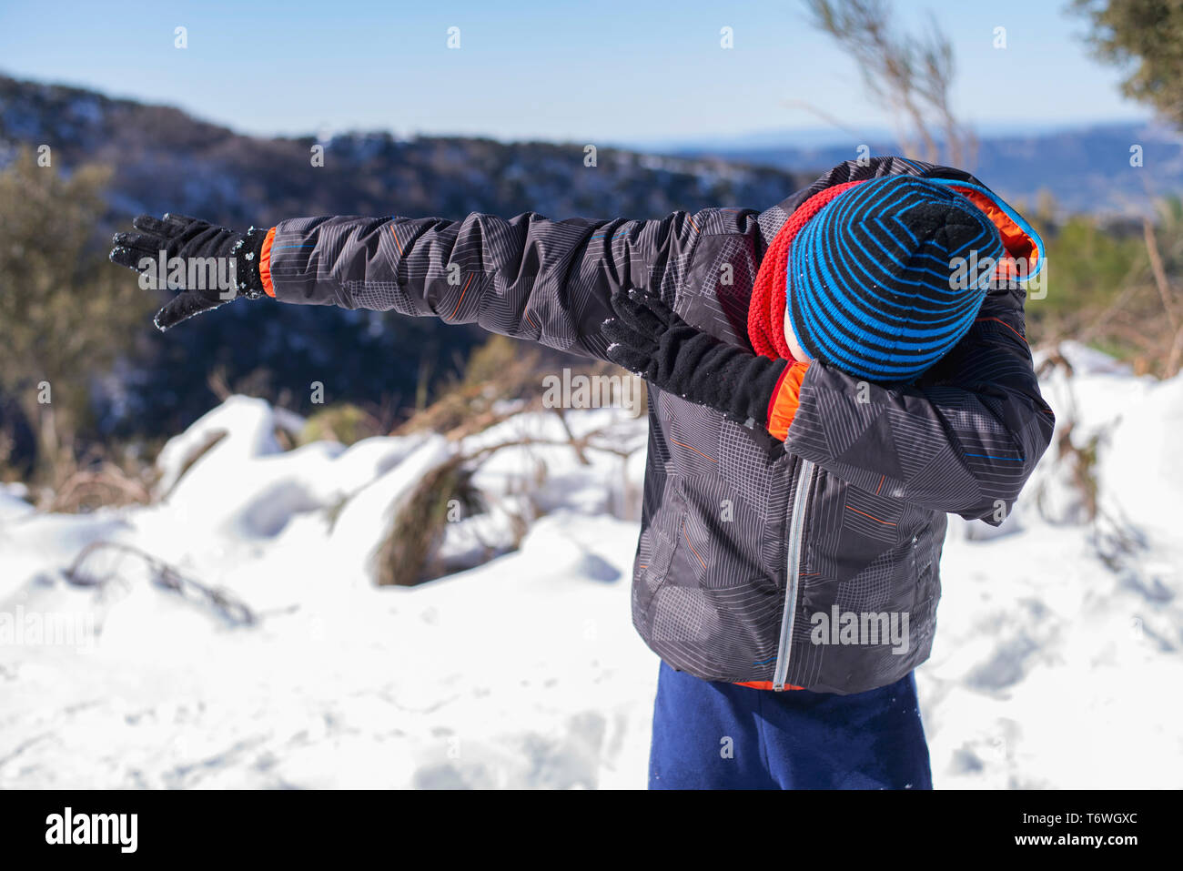 Front view of young boy performing a dab, standing on a snow mountain ...