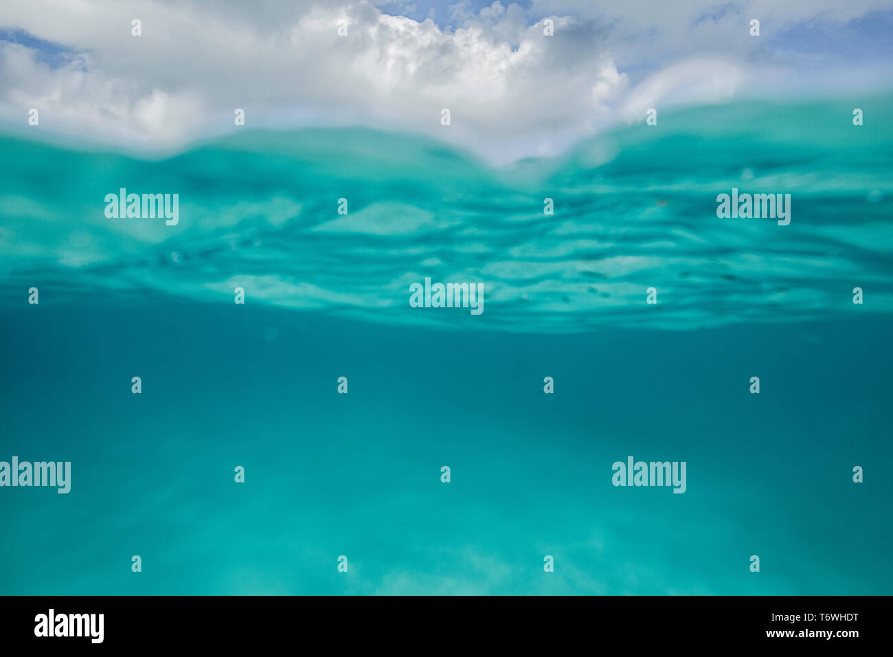 A split level shot of turquoise ocean water and clouds in a blue sky ...