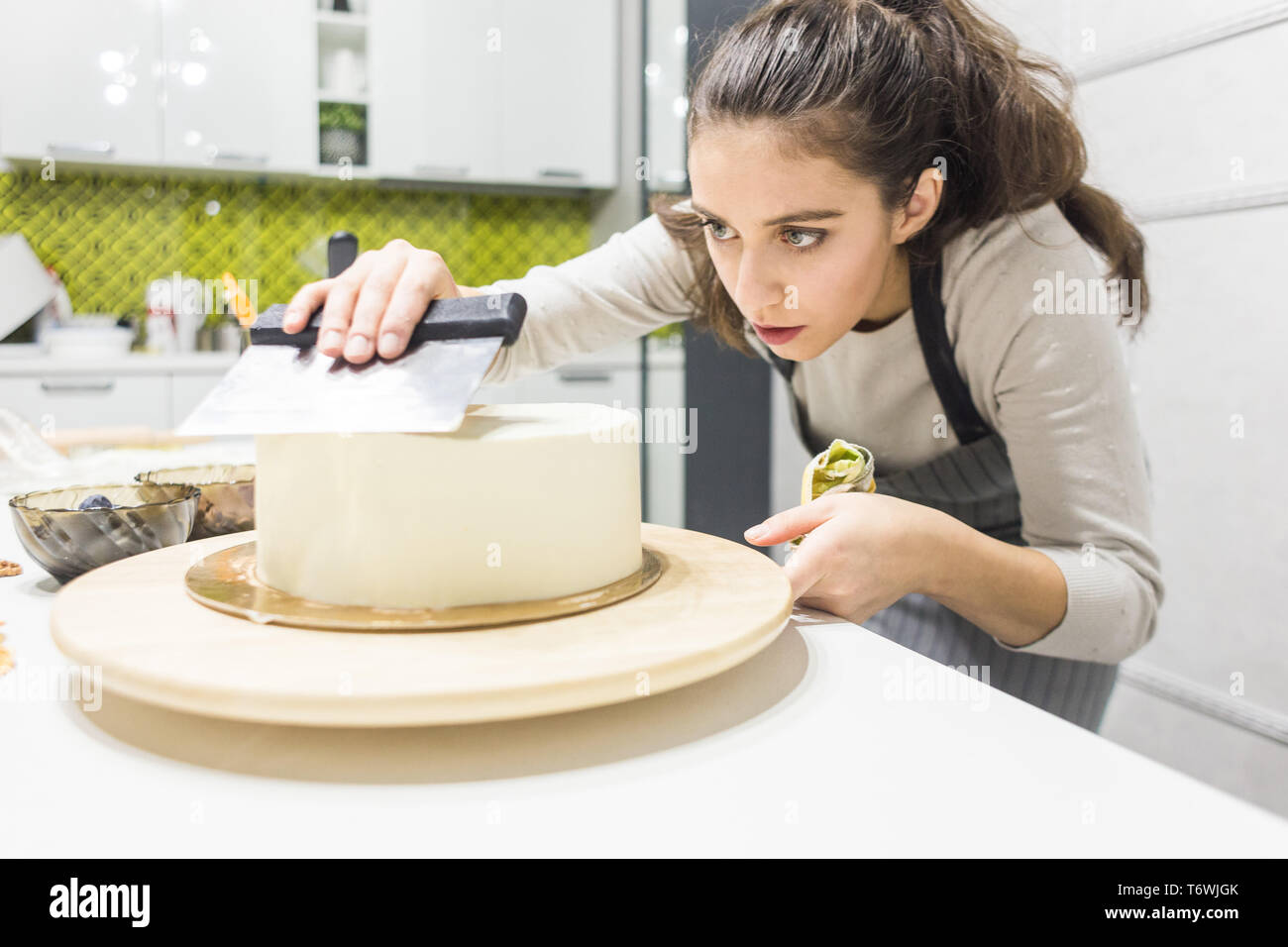 Confectioner smooths white cream on a biscuit cake with a cooking ...