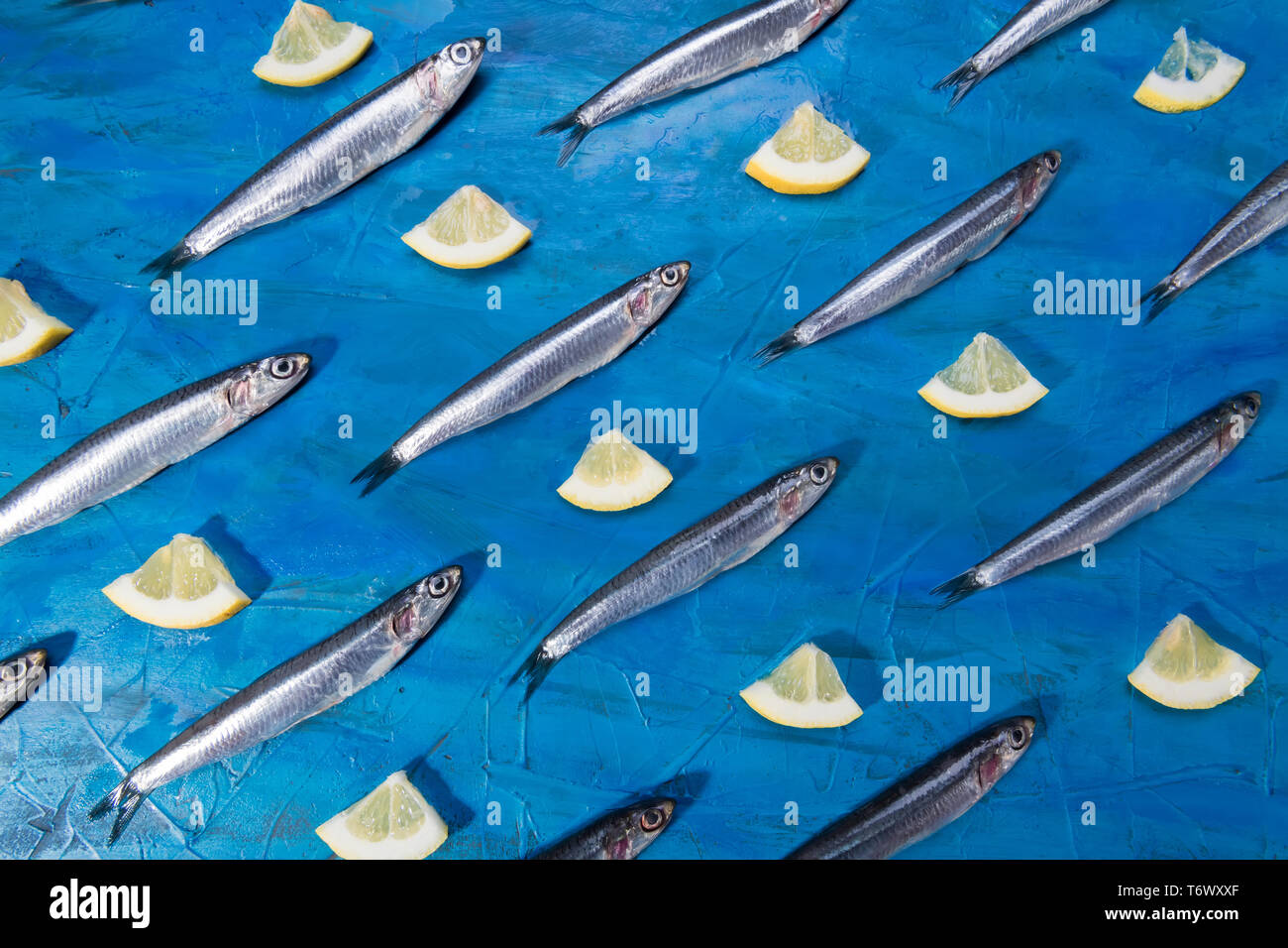 Fish pattern. Anchovies with slice of lemon on a black stone on a blue ...