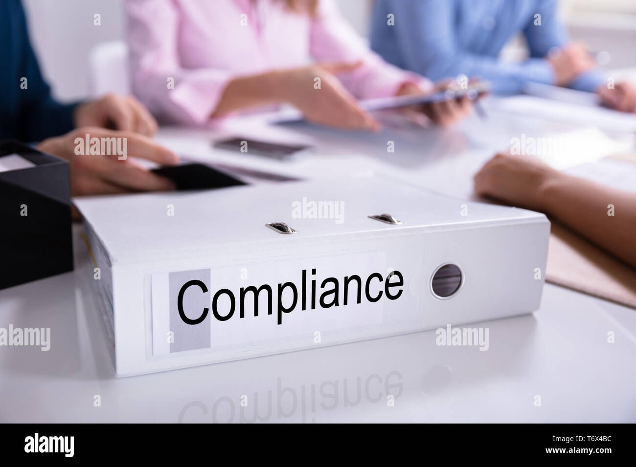 Businesspeople Sitting Near Compliance Documents Over Reflective Desk ...