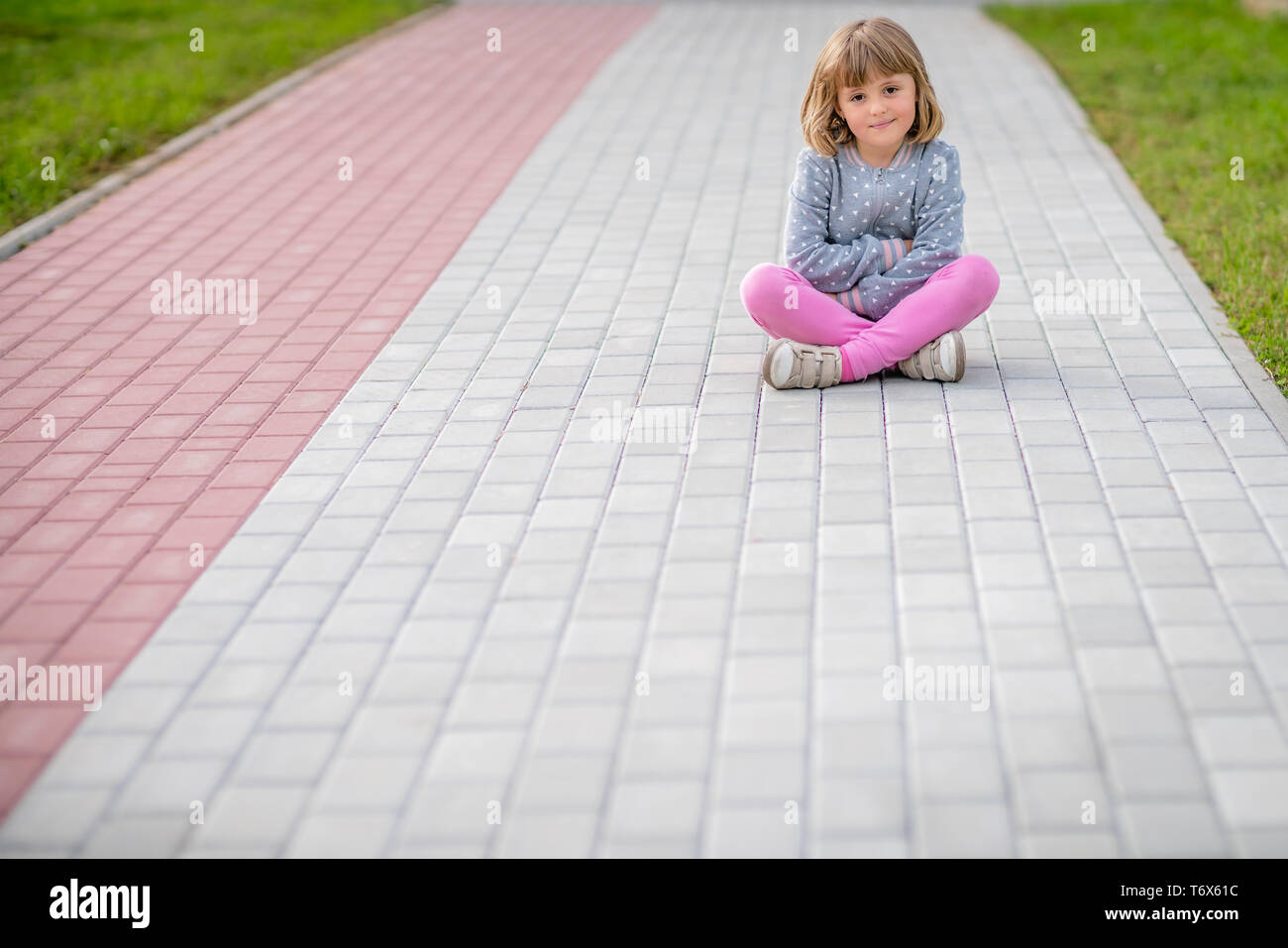Cute little girl sitting on a pavement Stock Photo - Alamy