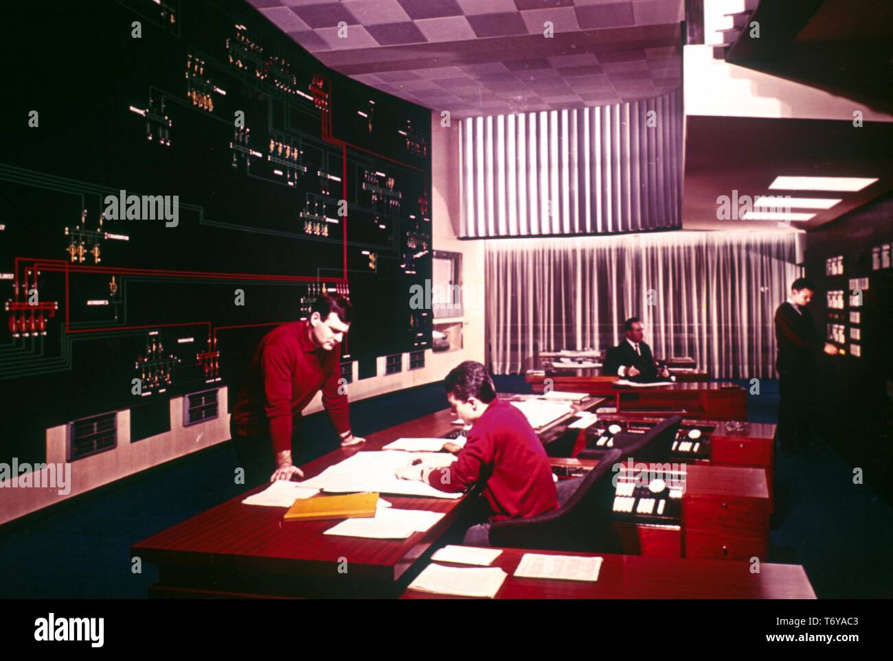 Four men stand and sit at desks while working in a nuclear power plant ...