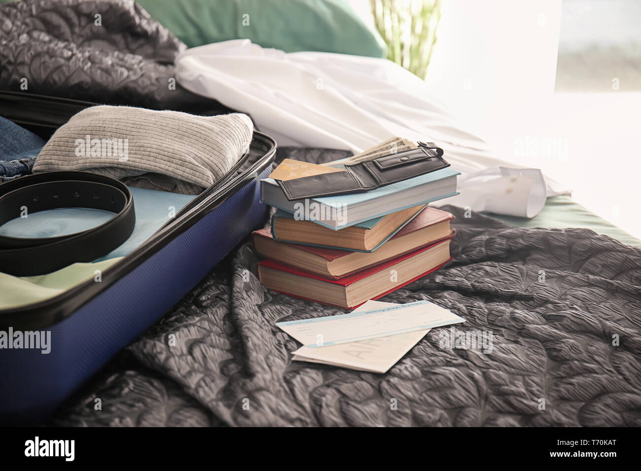 Wallet, documents and open suitcase with packed things on bed Stock ...