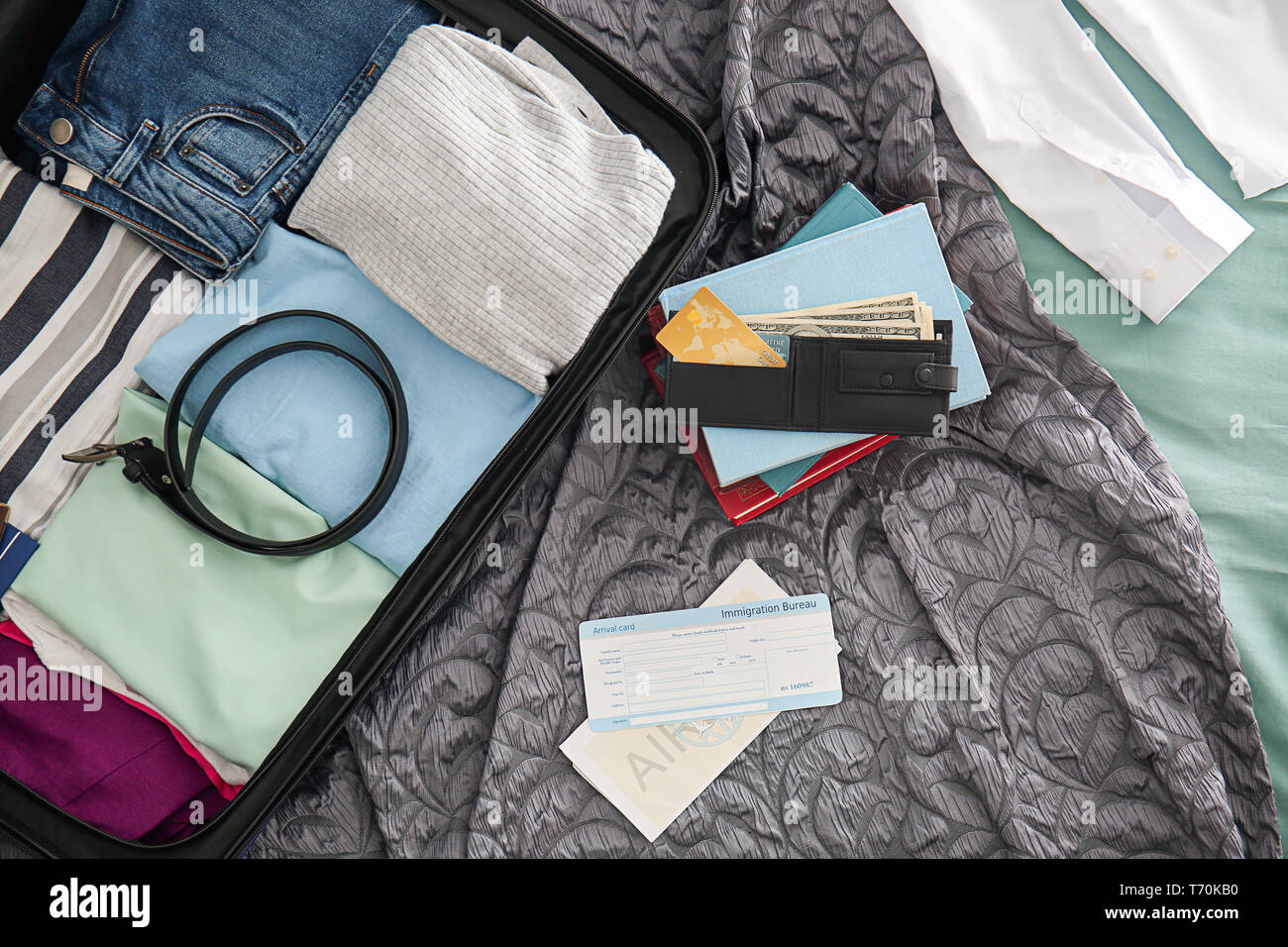 Wallet, documents and open suitcase with packed things on bed, top view ...
