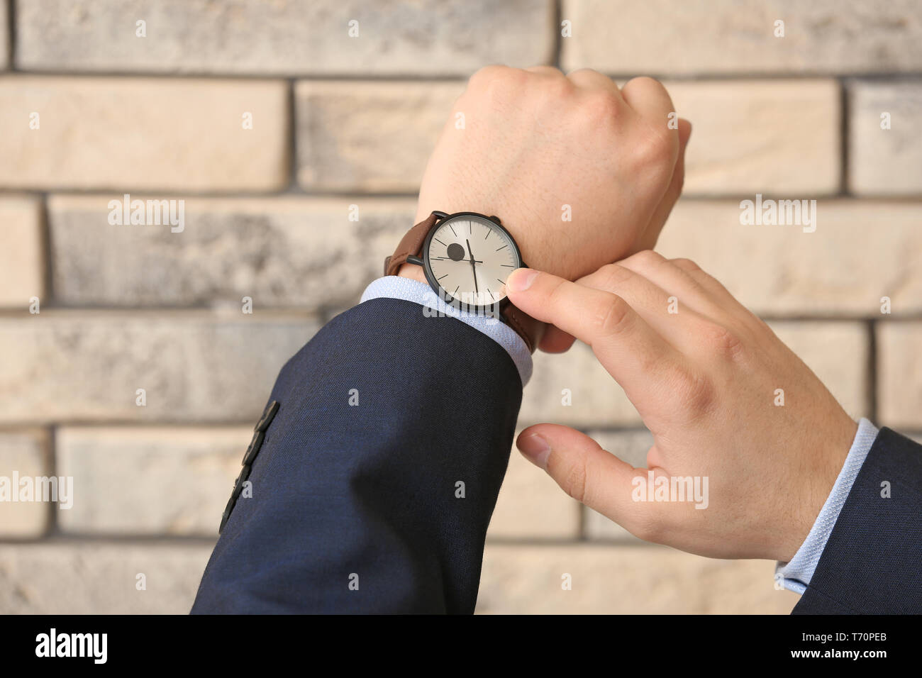 Man looking at his watch on brick background, closeup. Time management ...