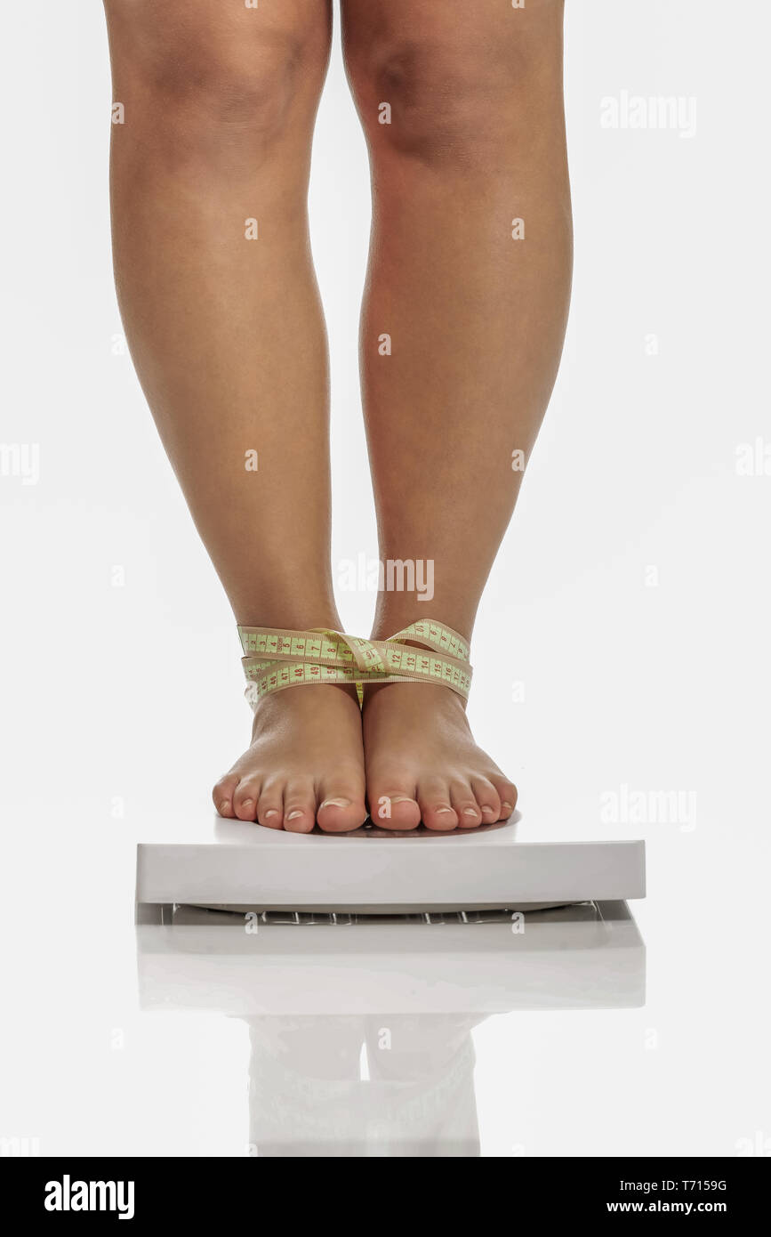 Oversize woman legs standing on weight with measure tape wrapped on ...