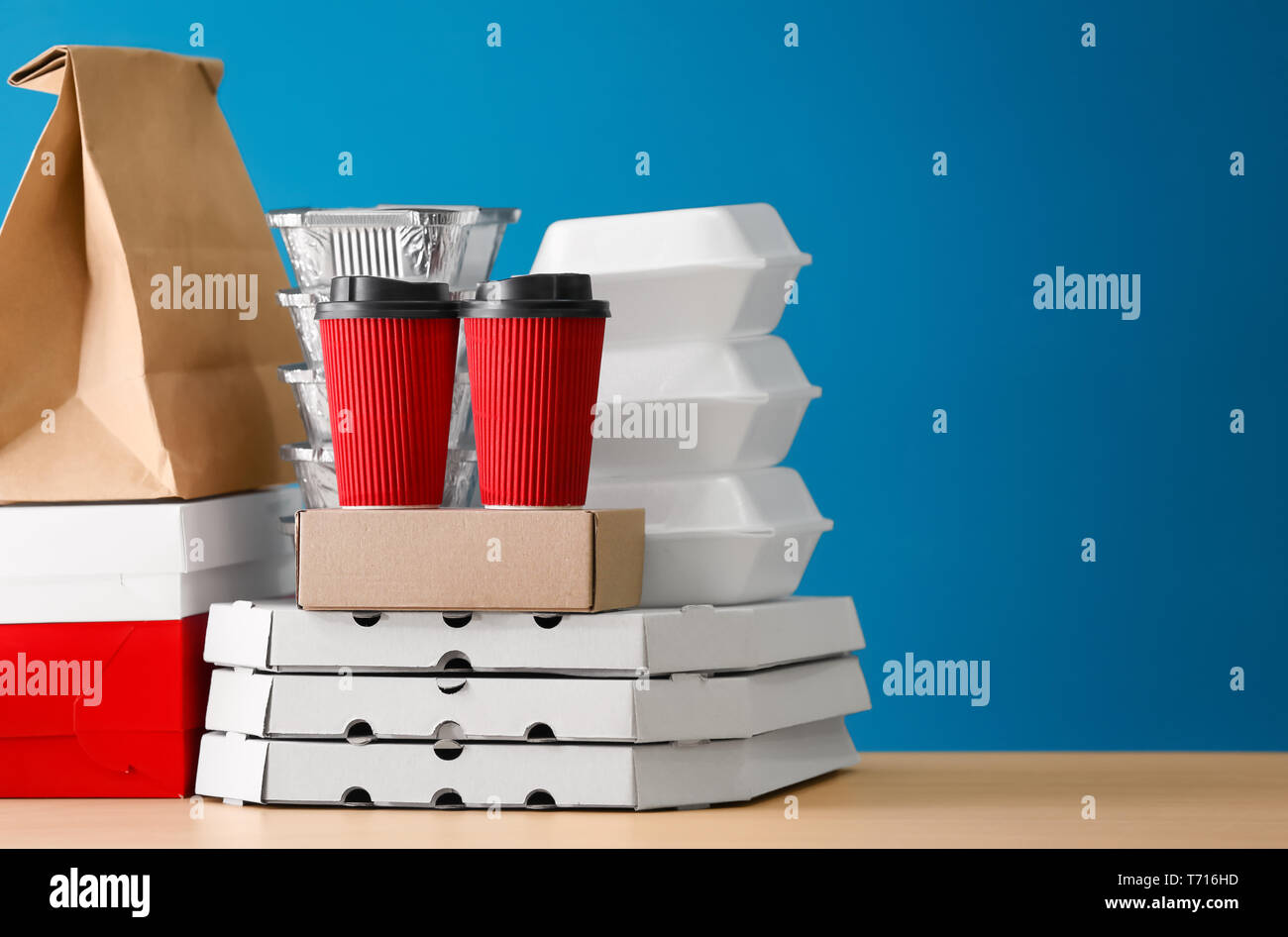 Different packages and carton cups on table against color background ...